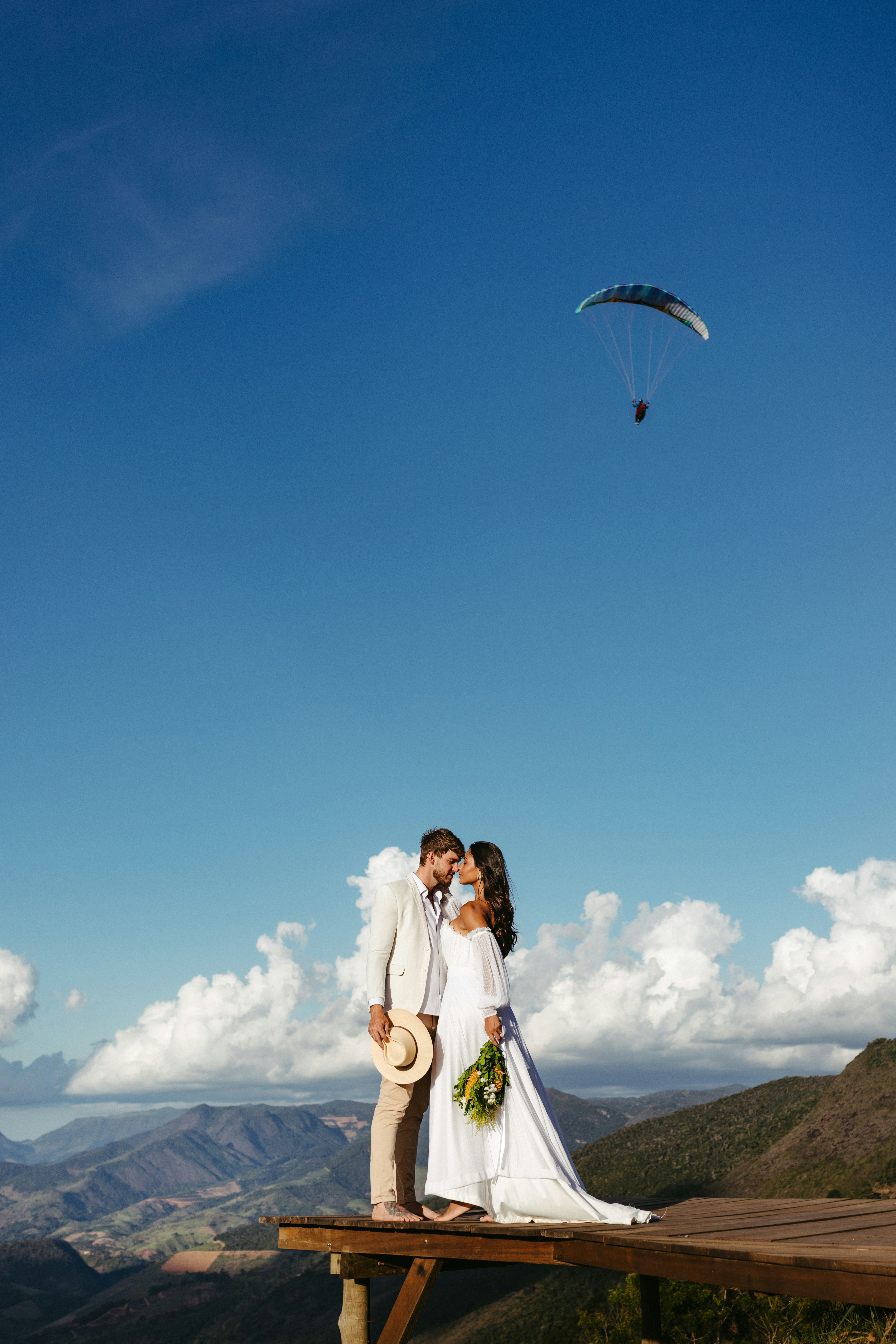 A bride and groom standing on a wooden platform with a parasail in the