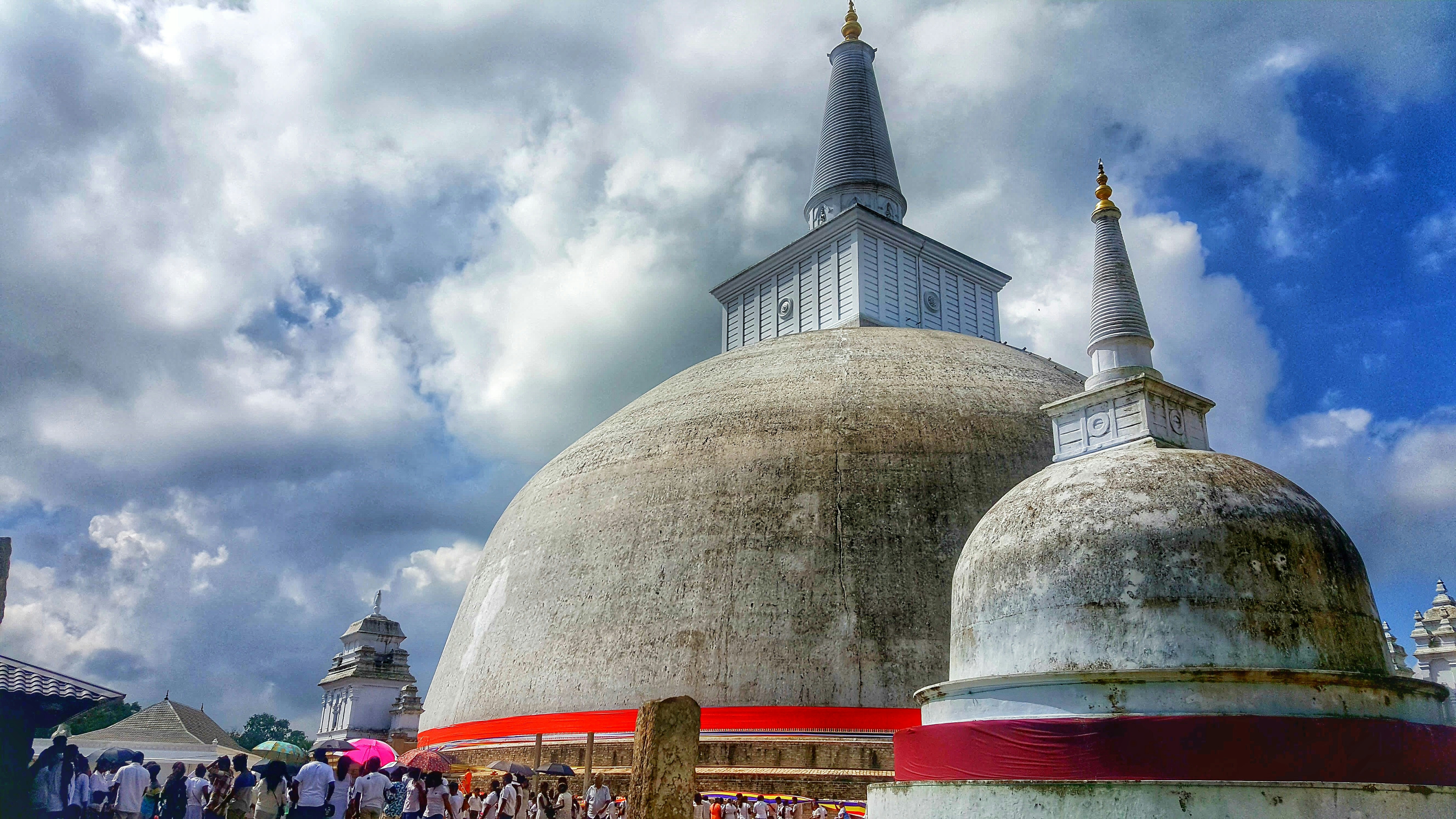 Large dagoba with spires against a backdrop of swirling clouds and a crowd of visitors below.
