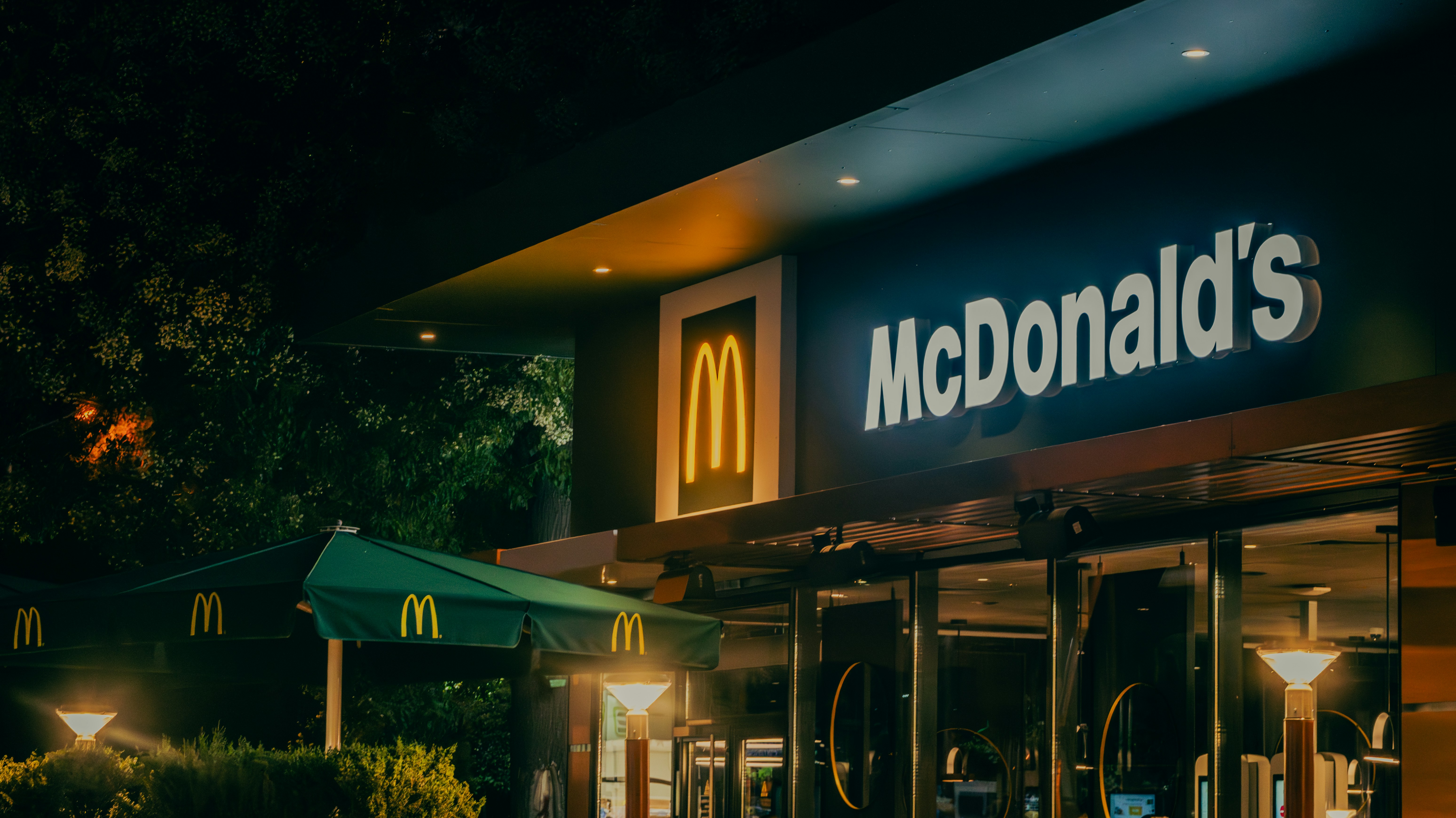 Illuminated McDonald's entrance with glowing signage and outdoor seating at night.