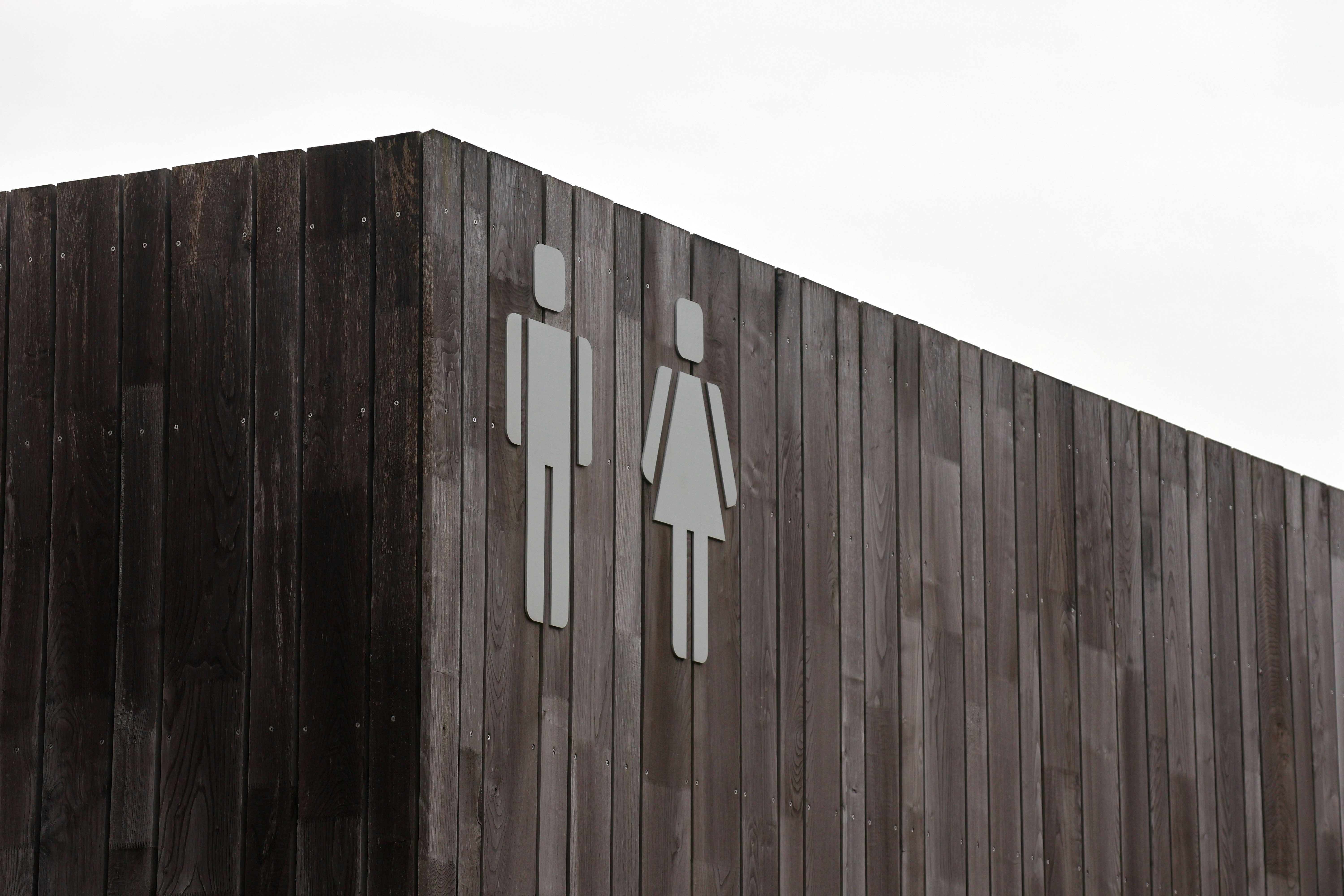 Weathered Slats, Quiet Icons: Restroom Signage on a Darkwood Facade