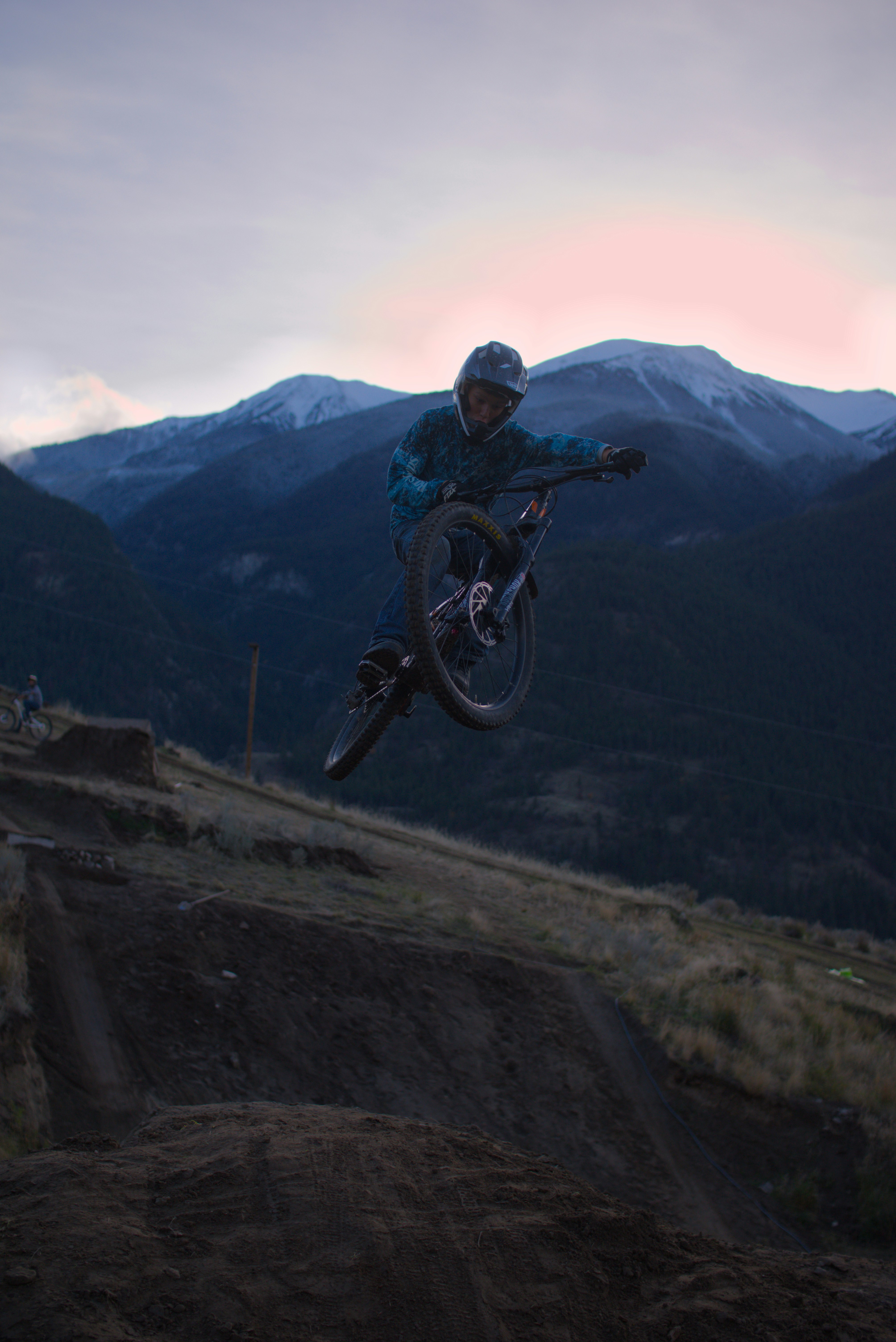 Airborne on the Ridge: Mountain Biker Clears a Dusk Jump with Snowy Peaks in the Background