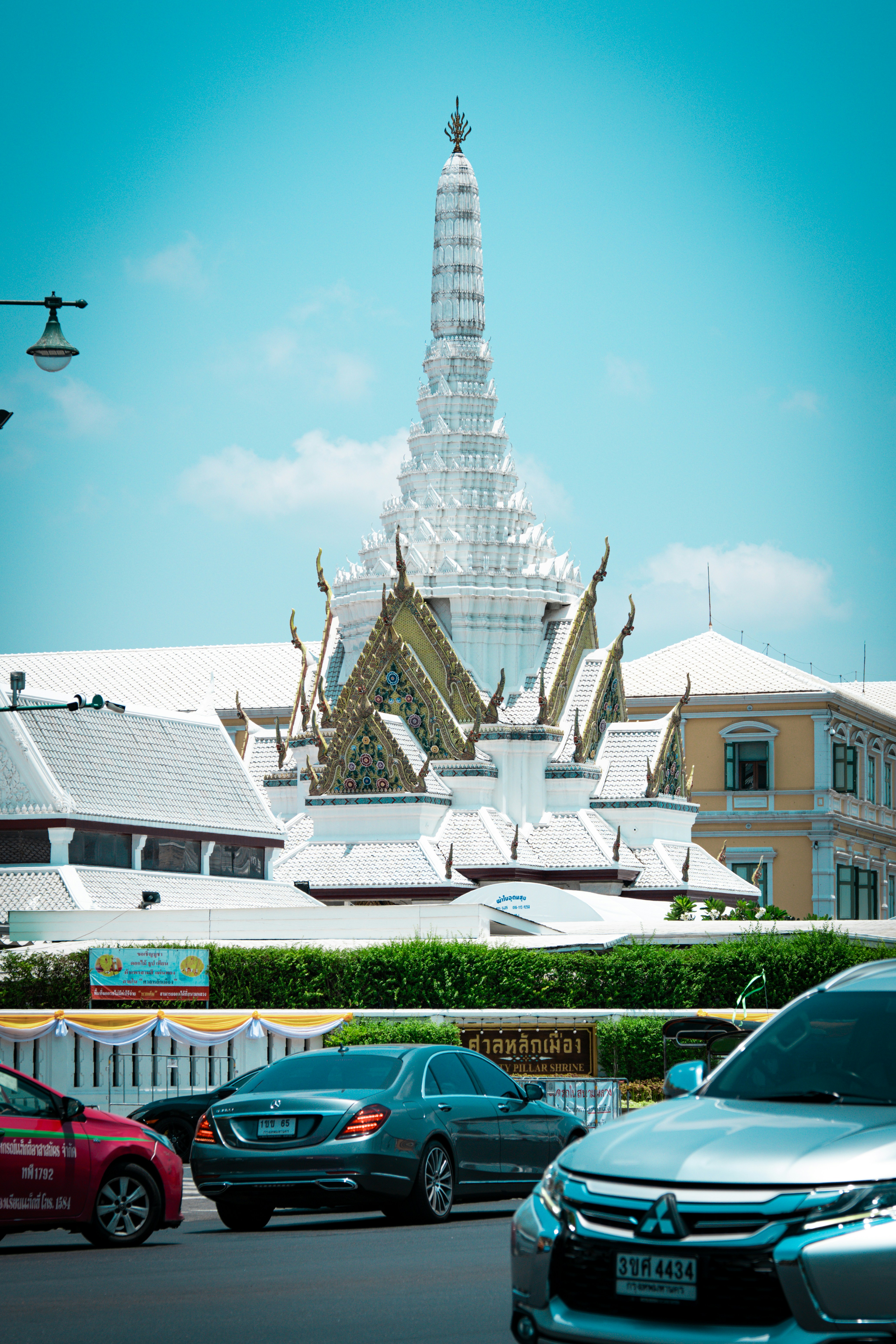 Intricate temple spire rises above a bustling street with cars in Bangkok under a vibrant blue sky.