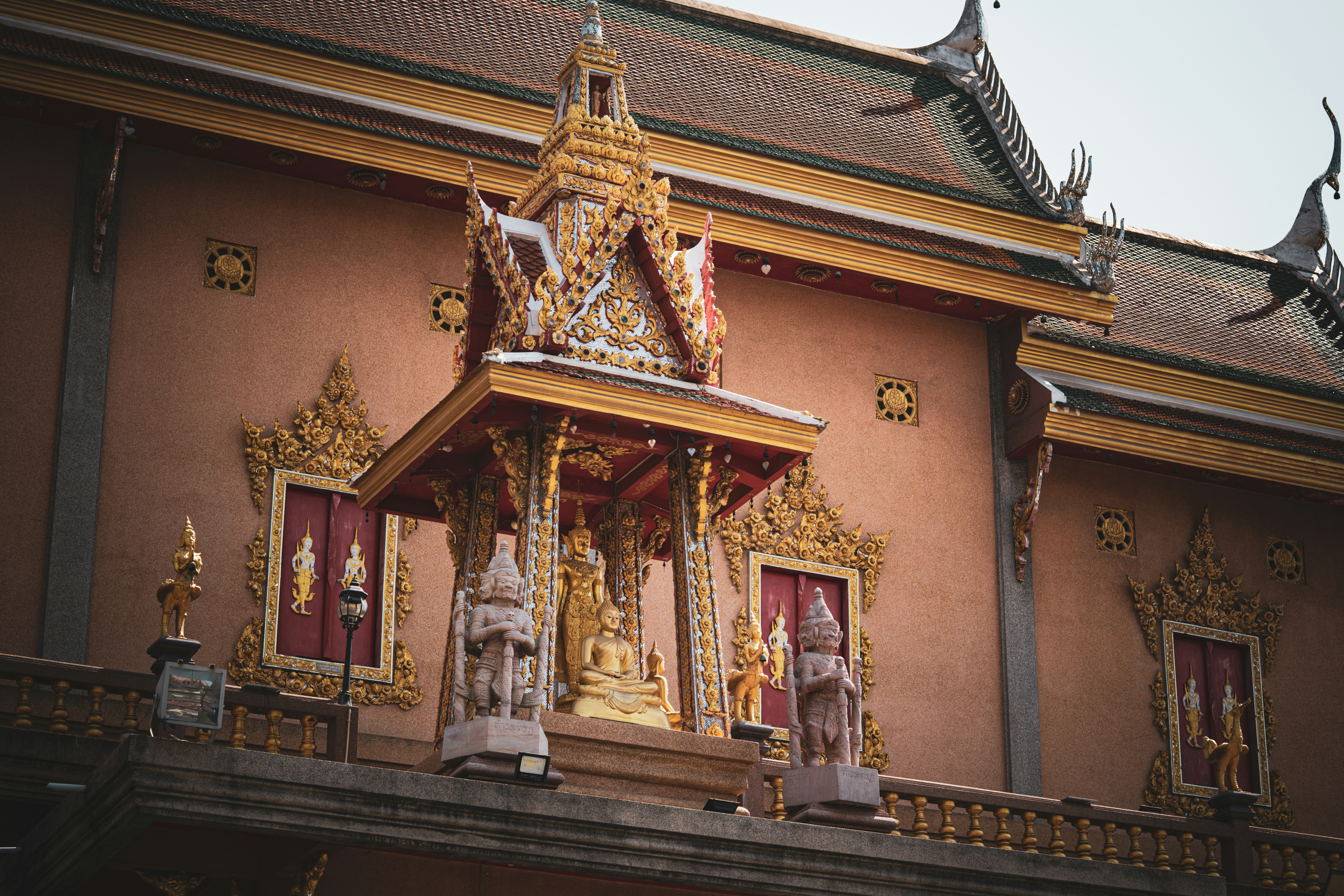 Ornate temple facade with intricate gold carvings and red accents under a clear sky.