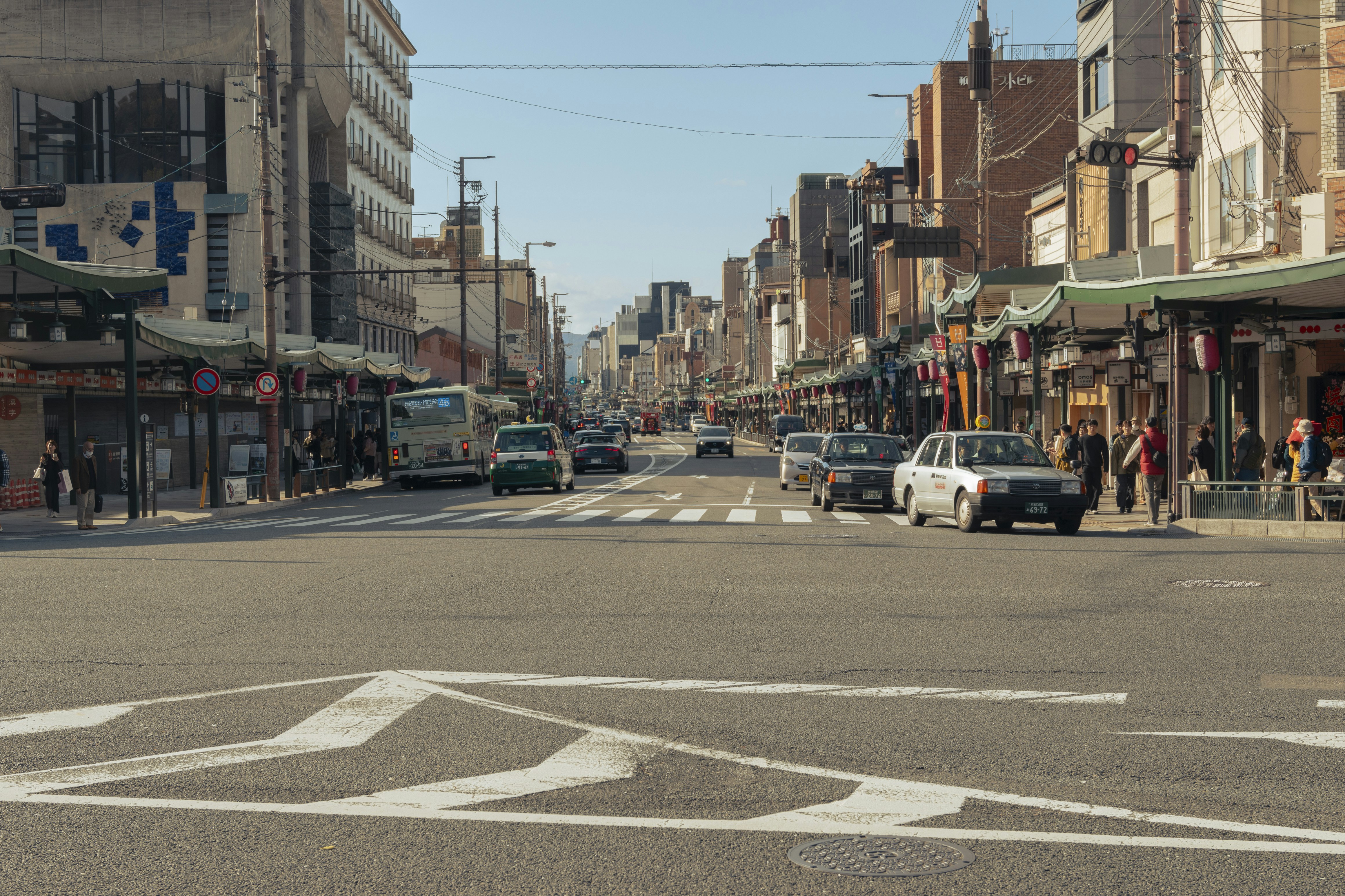 Busy city street in Kyoto with vehicles and pedestrians under a clear sky.