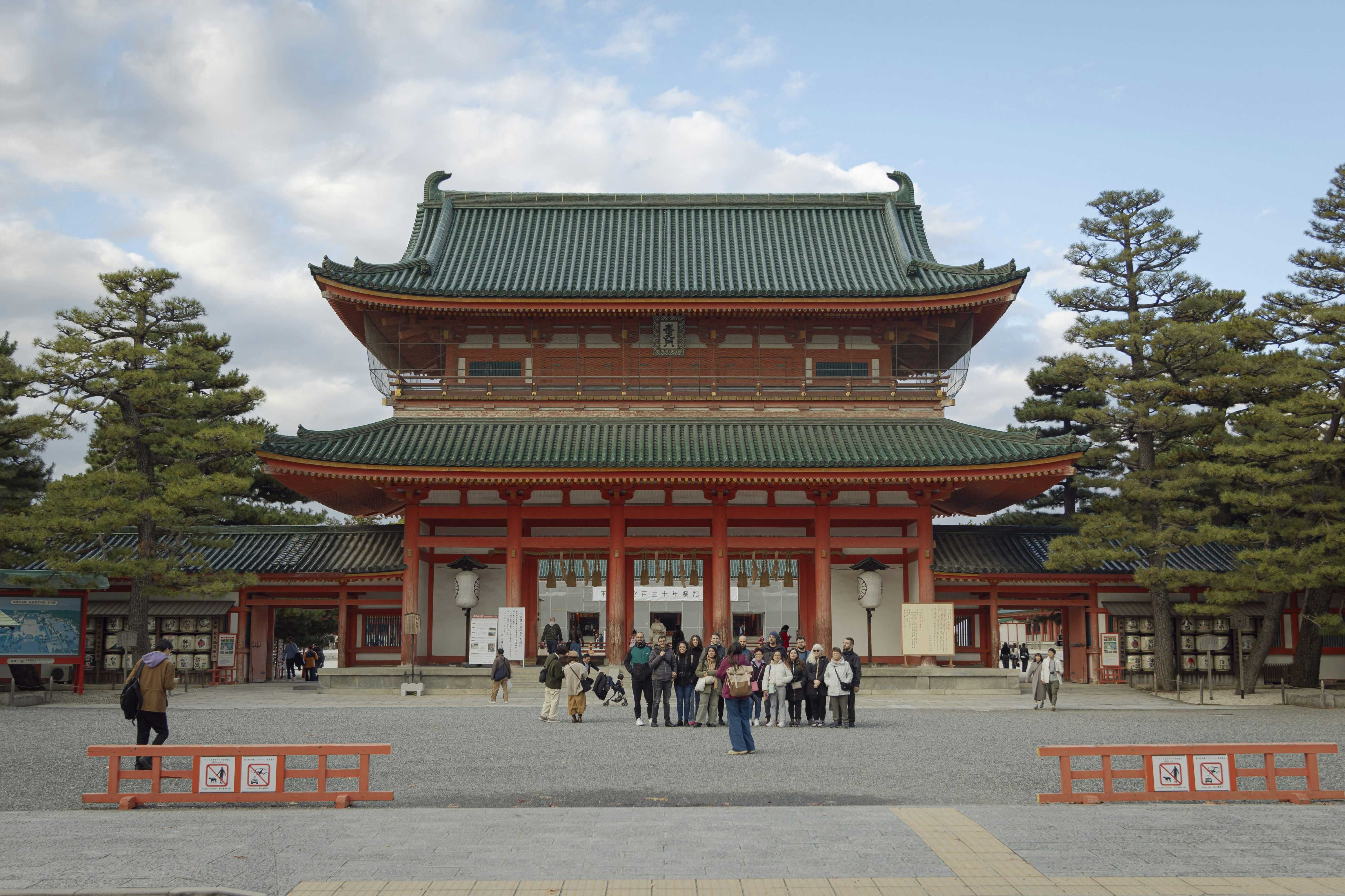 Group of people standing in front of a traditional Japanese temple with green-roofed structure and red accents.