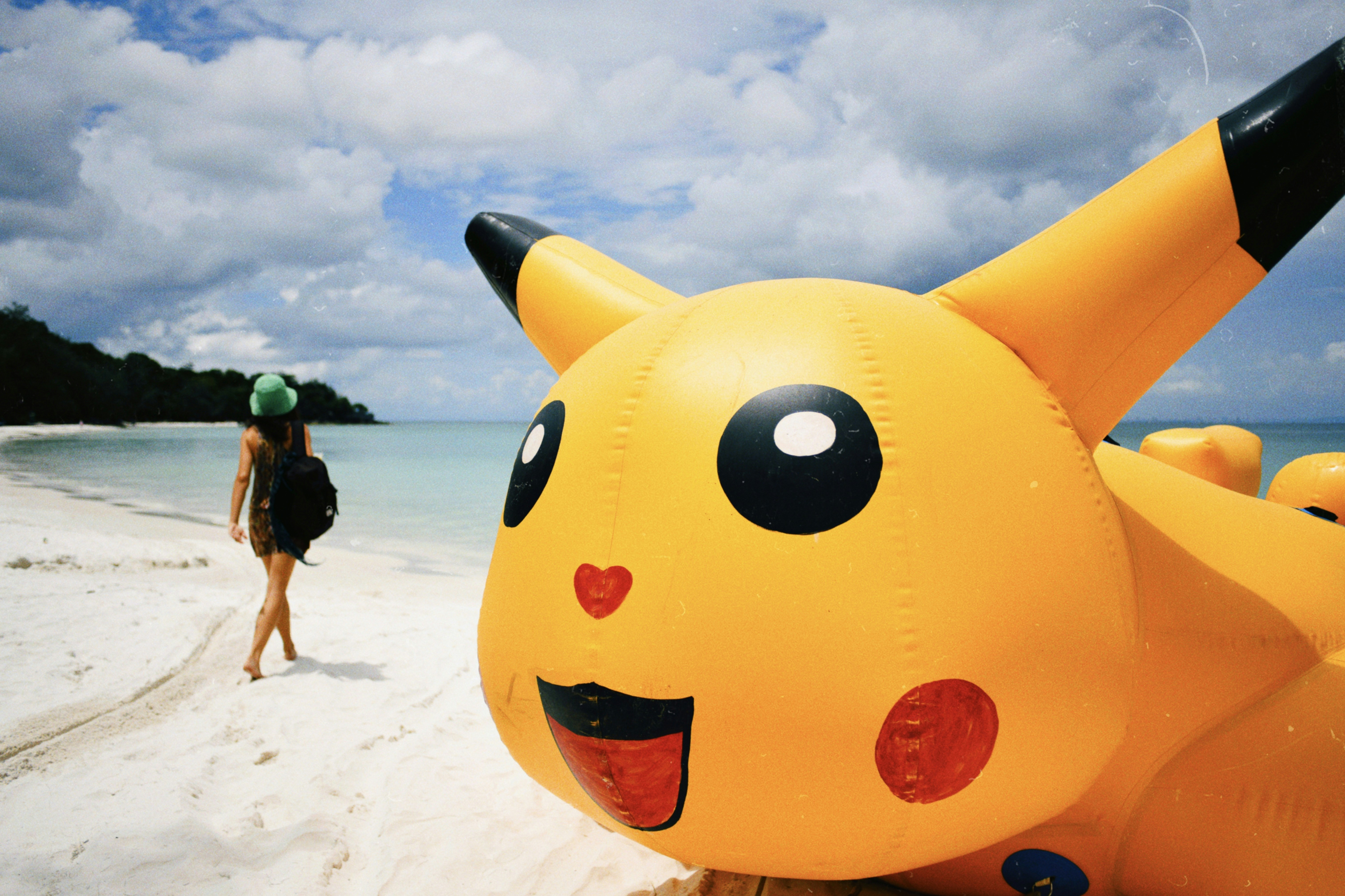A woman walking on a beach next to a large inflatable pikachu photo ...