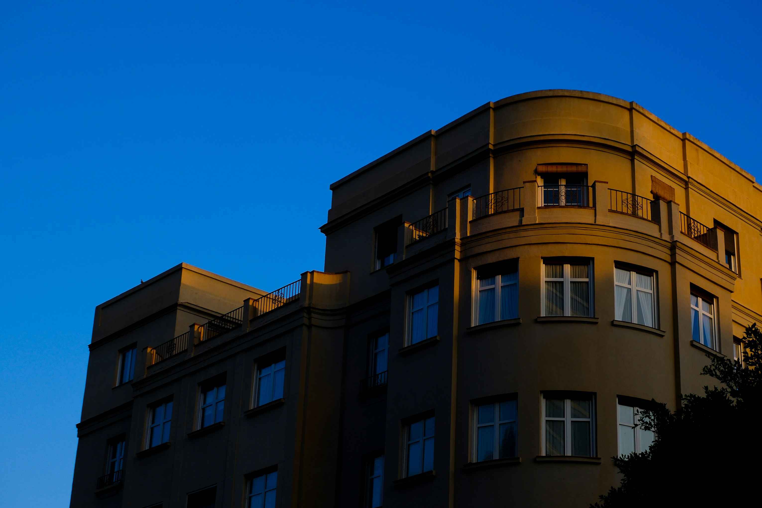 Sunset light casts warm hues on an urban building against a clear blue sky.
