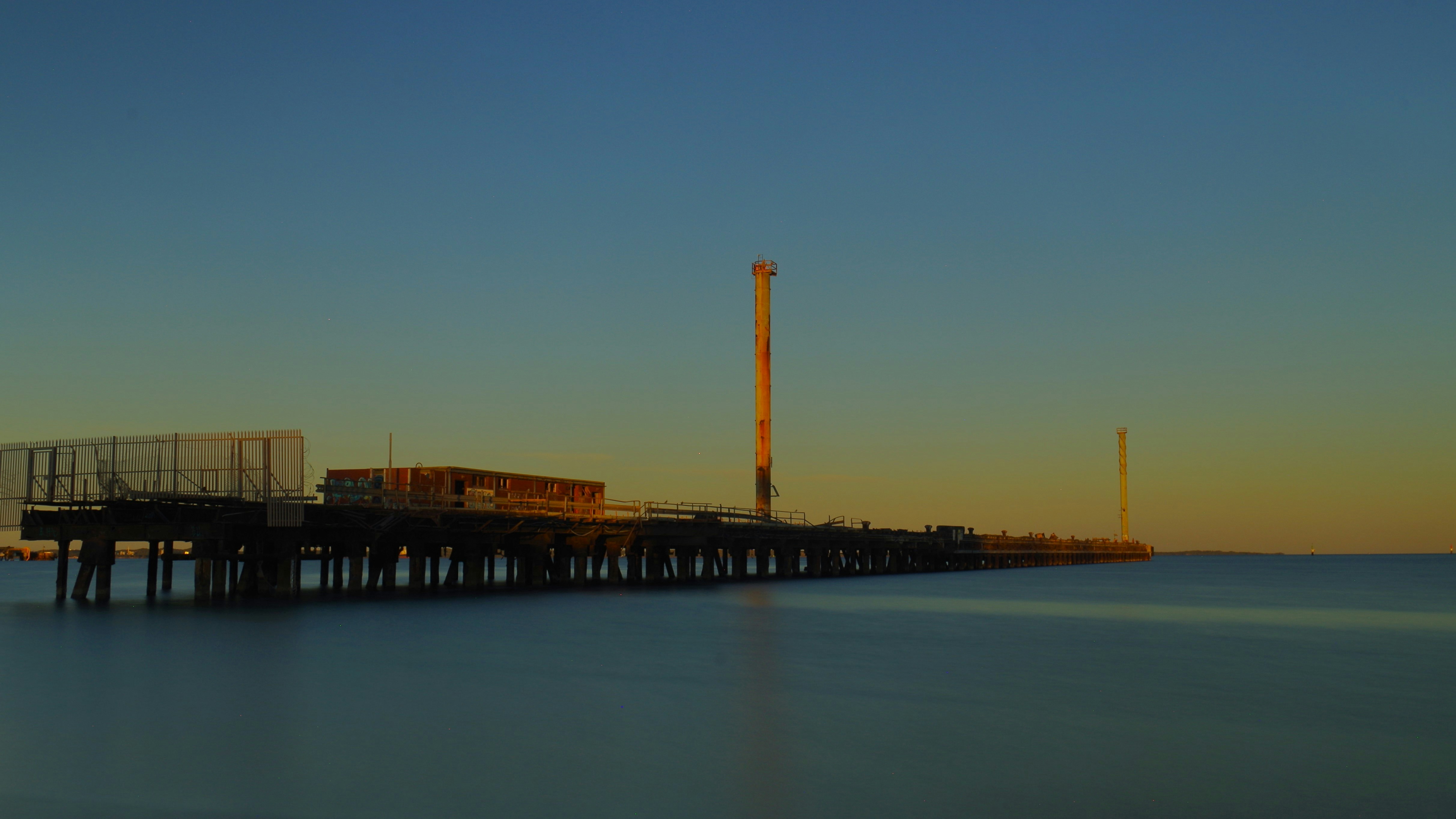 An old jetty stretches into calm waters under a twilight sky.