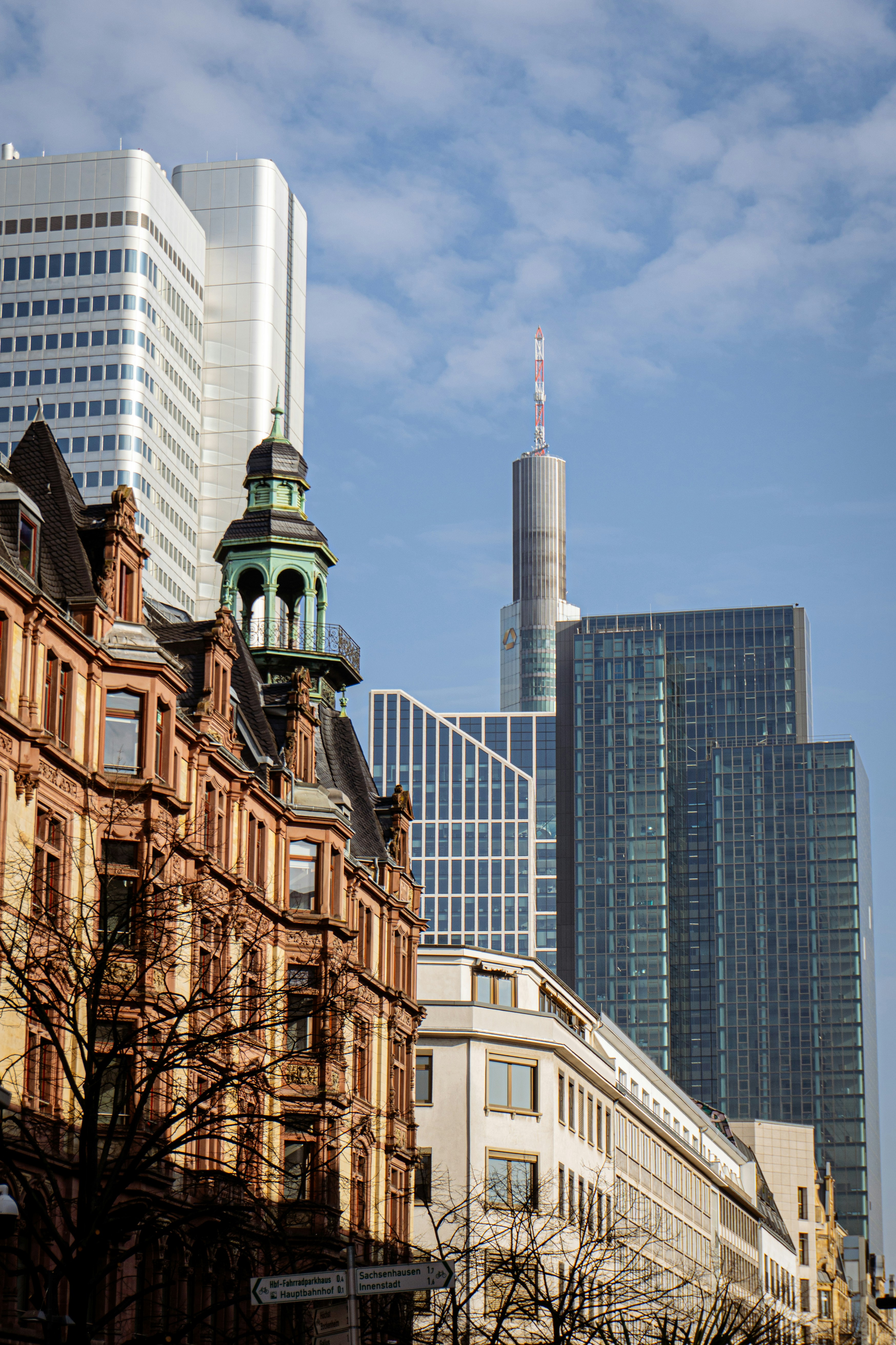 Classic European buildings with copper domes alongside modern skyscrapers under a clear blue sky.