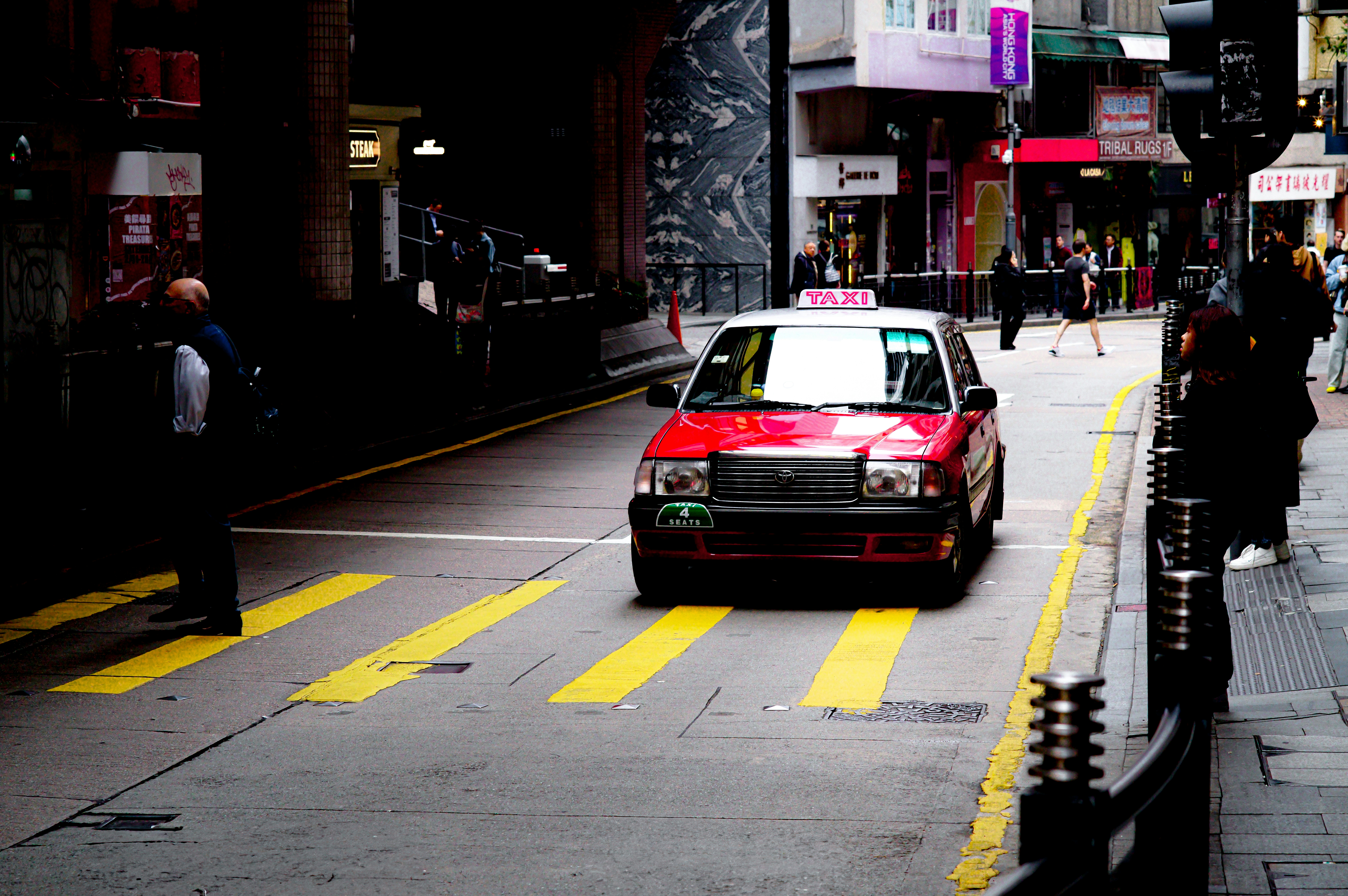 A red car driving down a street next to tall buildings