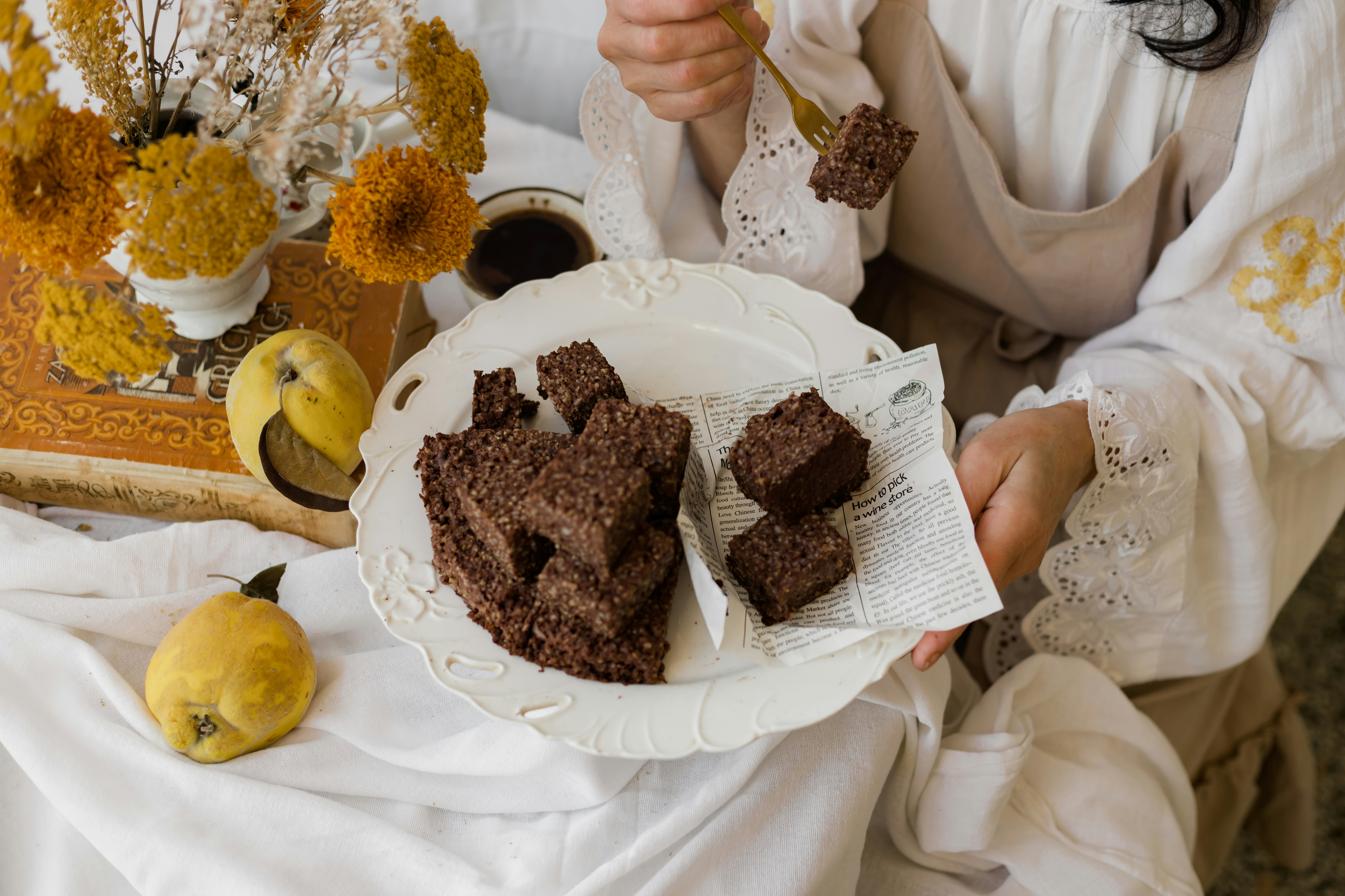 A plate of chocolate treats rests on a delicate napkin, accompanied by a cup of coffee and vibrant yellow flowers, creating a warm, inviting atmosphere.