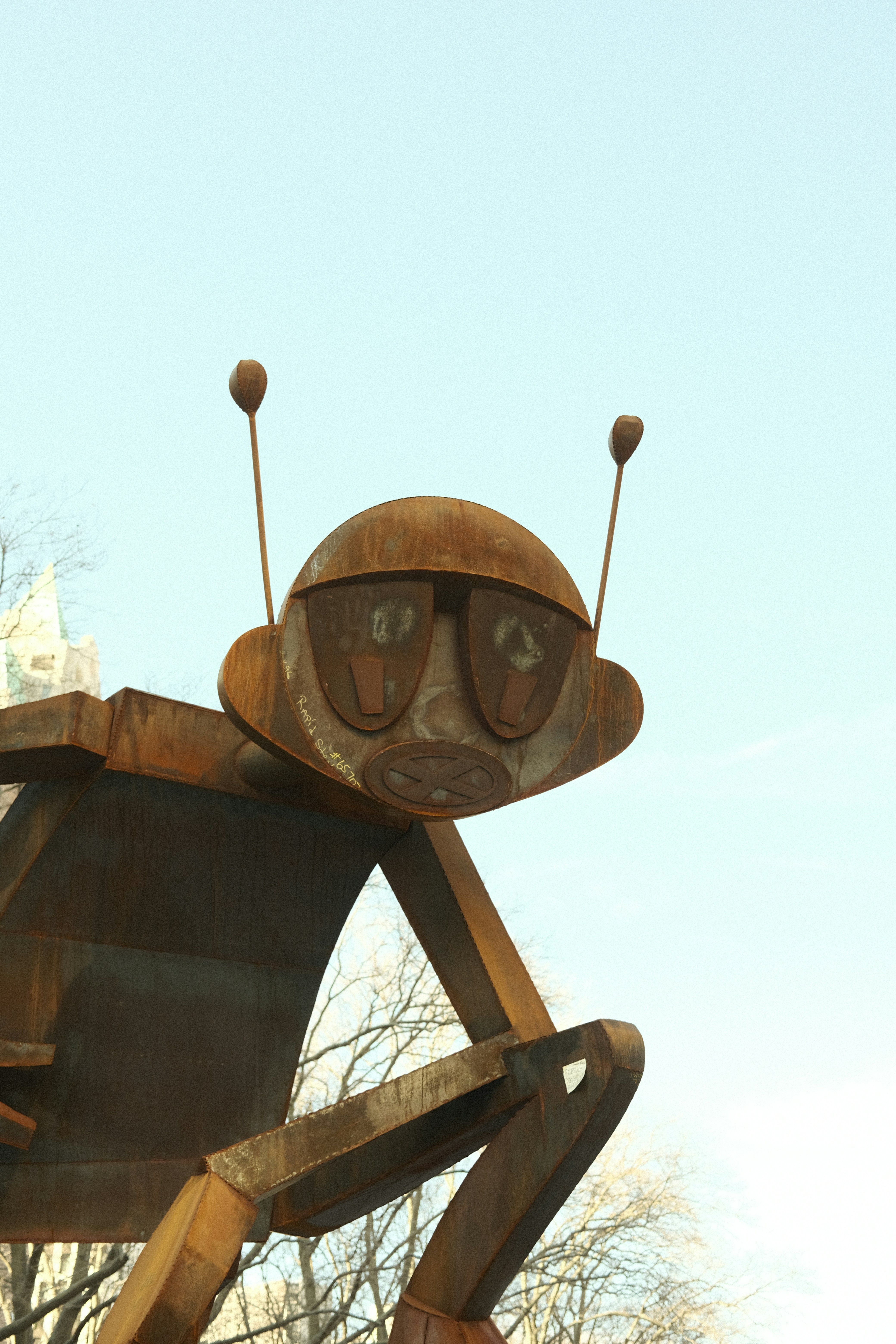 Rusting Sentinel: The Giant Grasshopper Sculpture Against a Pale Sky