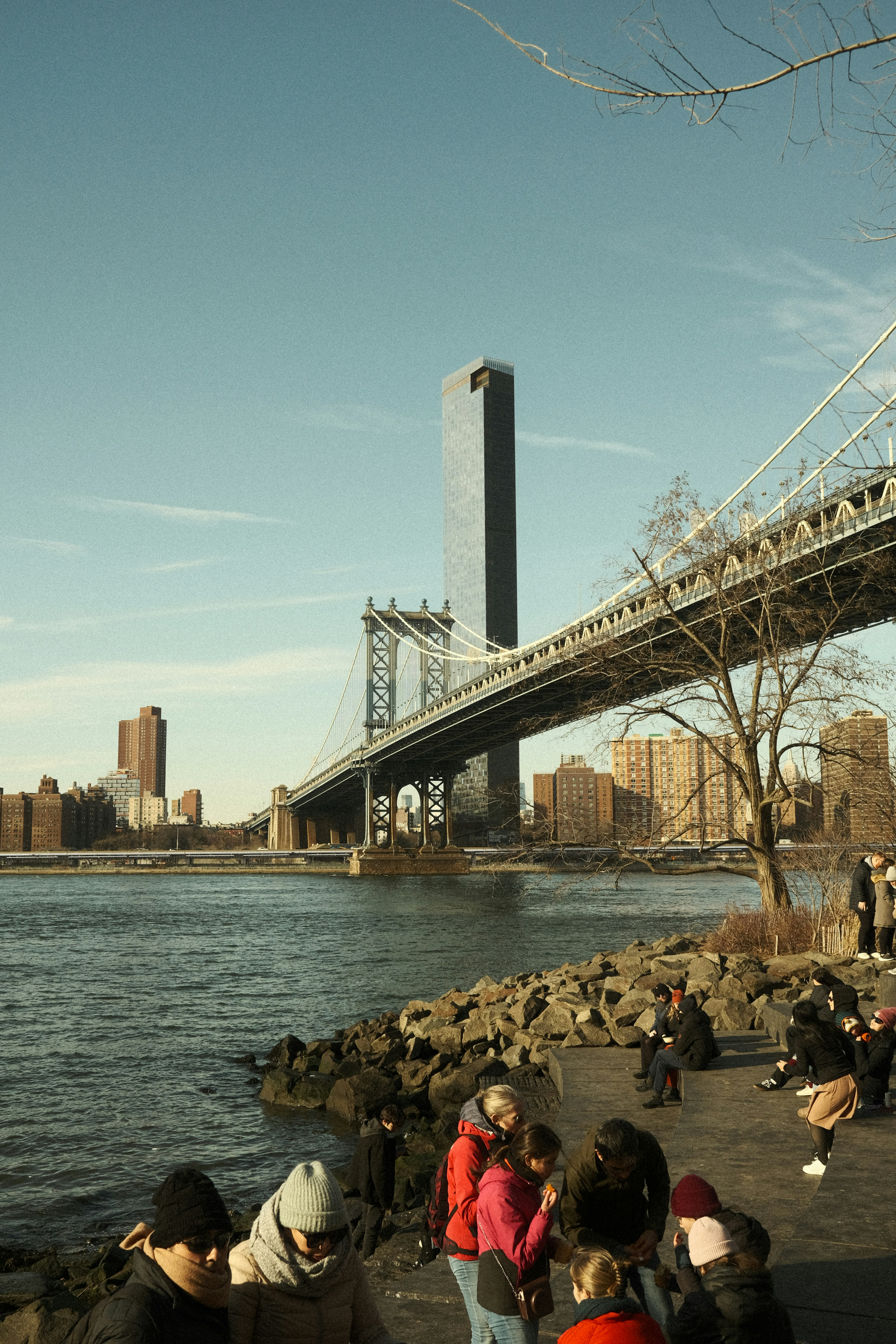 A group of people standing next to a river under a bridge