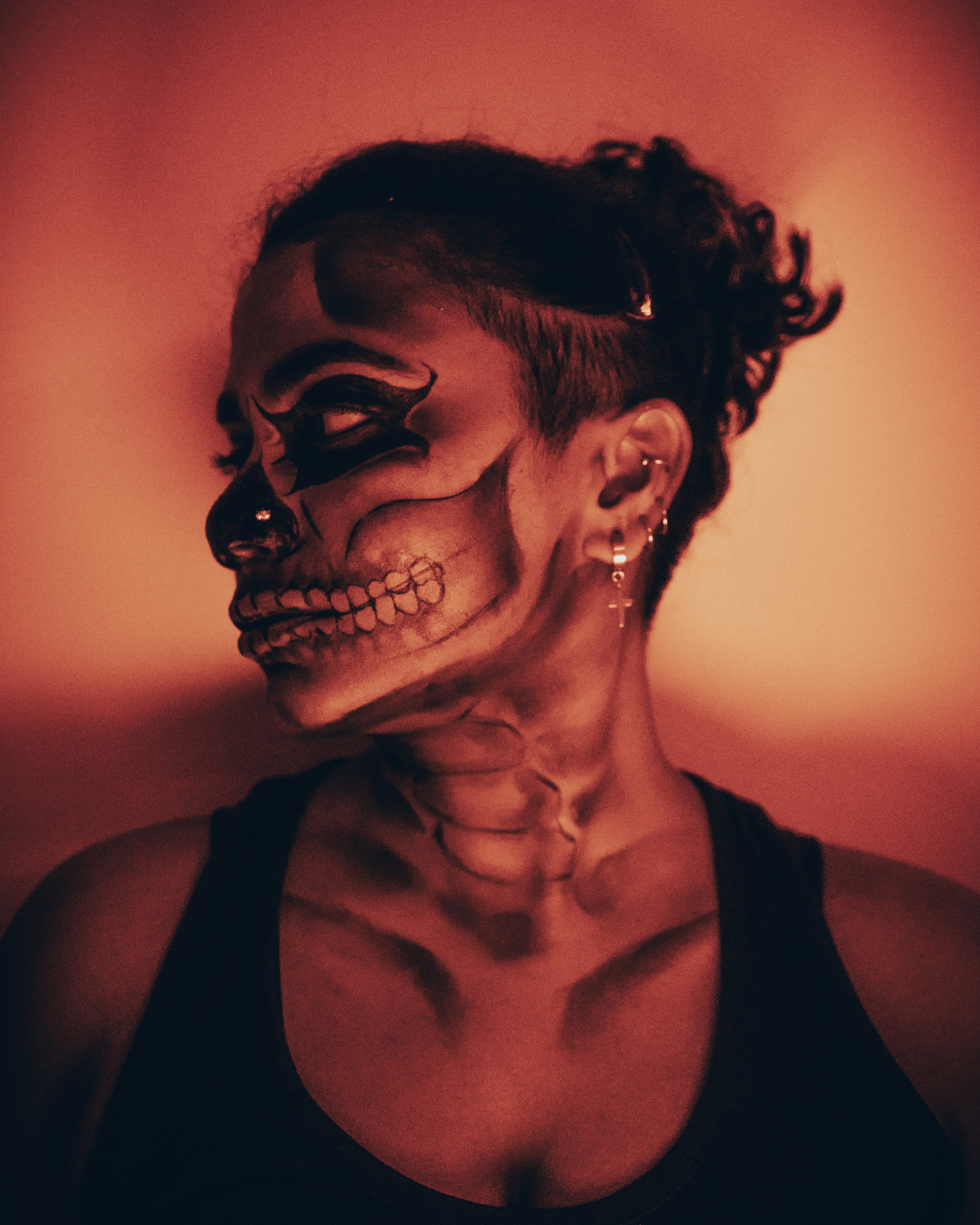 A side profile of a woman adorned with intricate skull face paint, set against a warm, glowing background. The artwork emphasizes her features and the haunting beauty of the design.