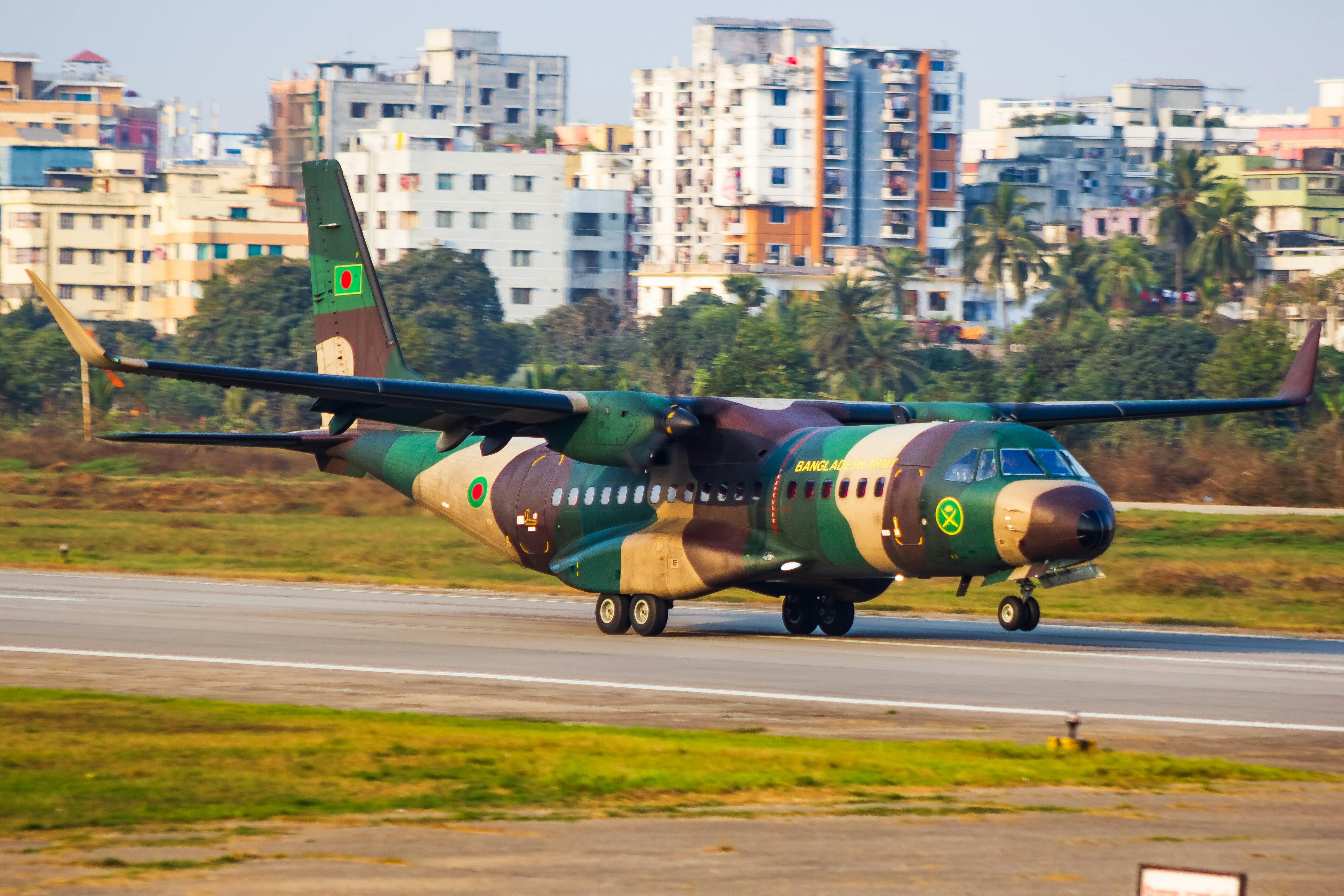 Camouflaged C-130-like Transport Slices the Runway with Urban Backdrop
