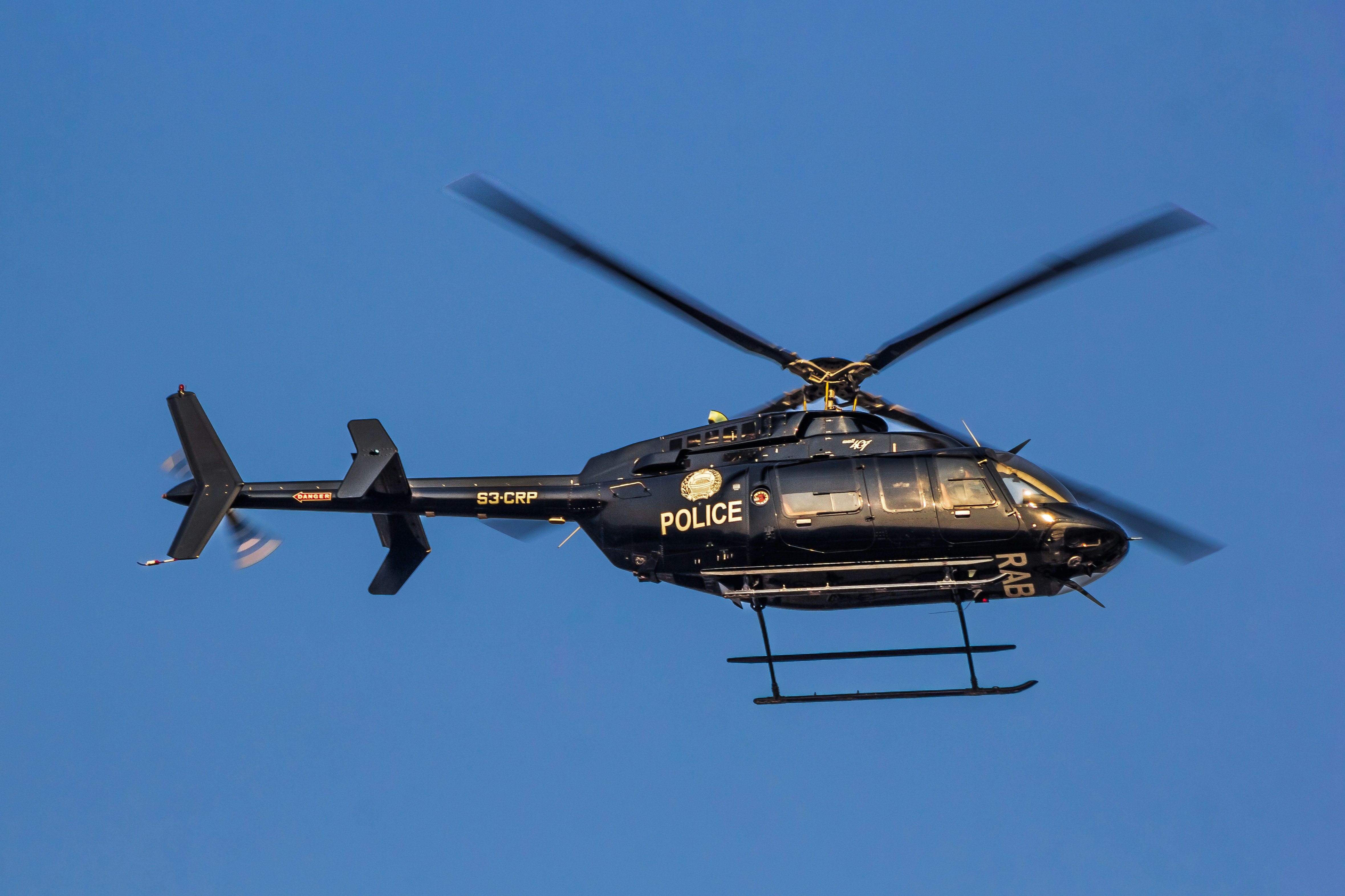 Midair Pursuit: Black Police Helicopter Cutting Through a Bright Blue Sky