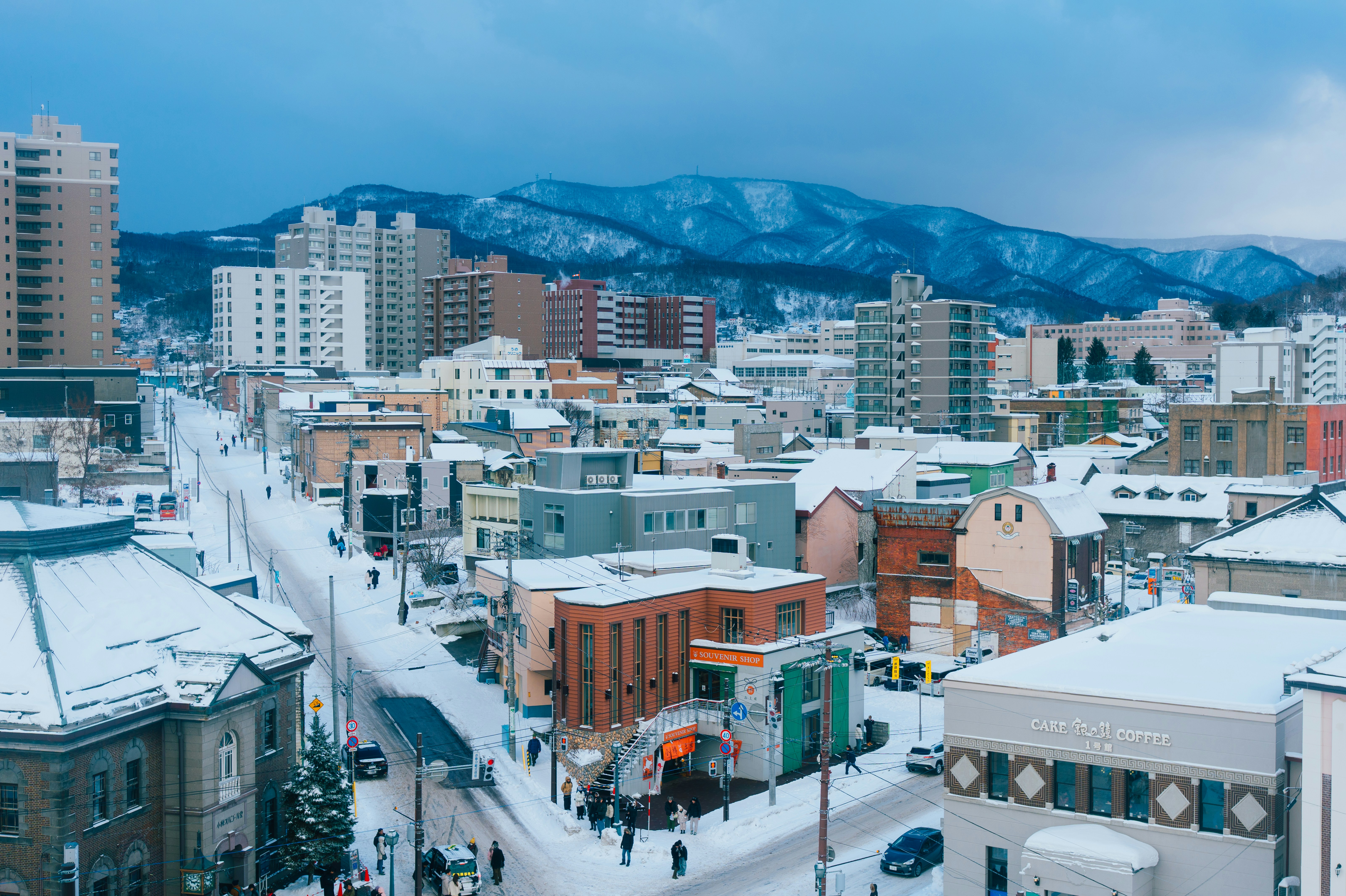Snow-covered cityscape with colorful buildings against a backdrop of mountains and cloudy sky.
