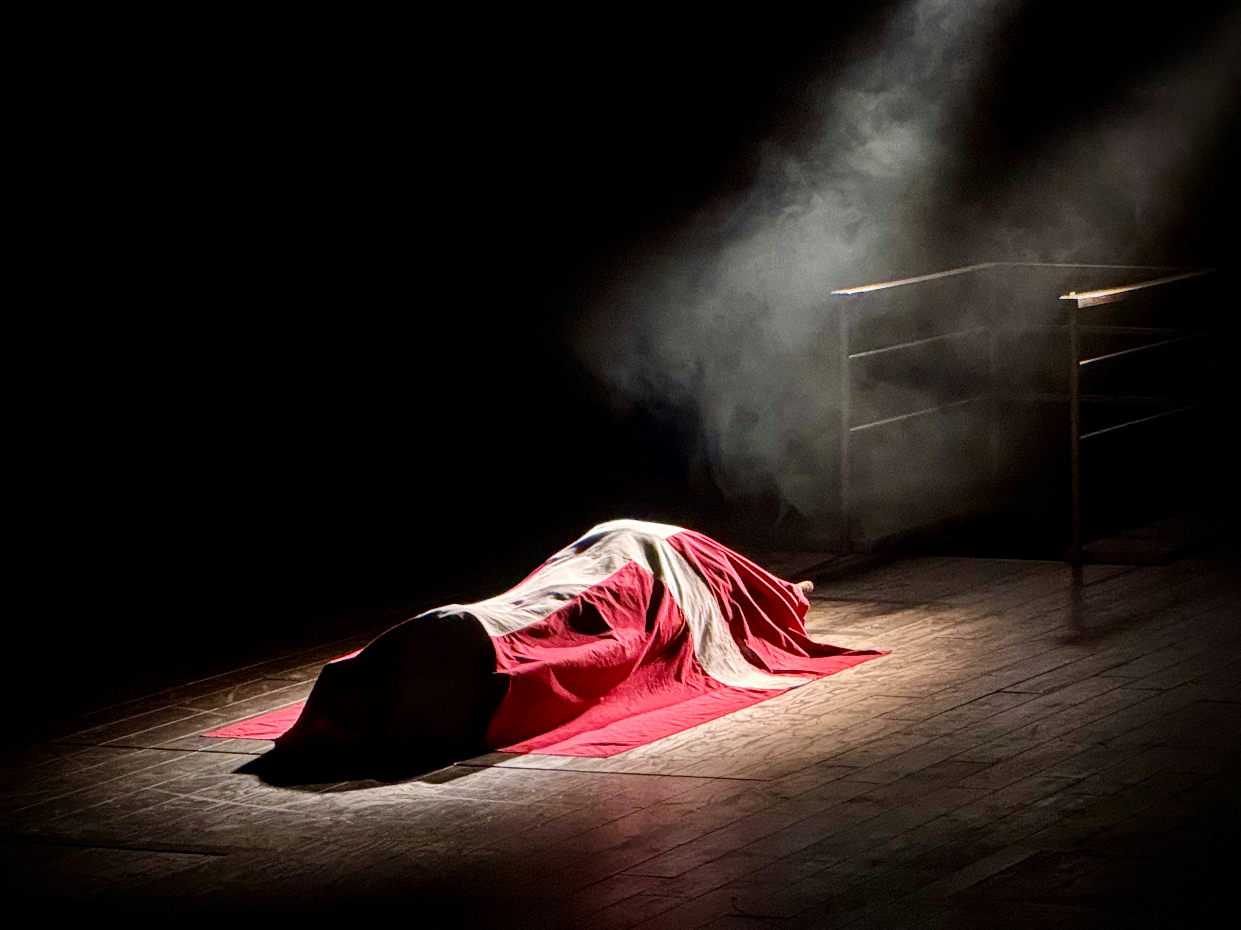 Red Draped Silhouette on a Sparse Stage Under Spotlight