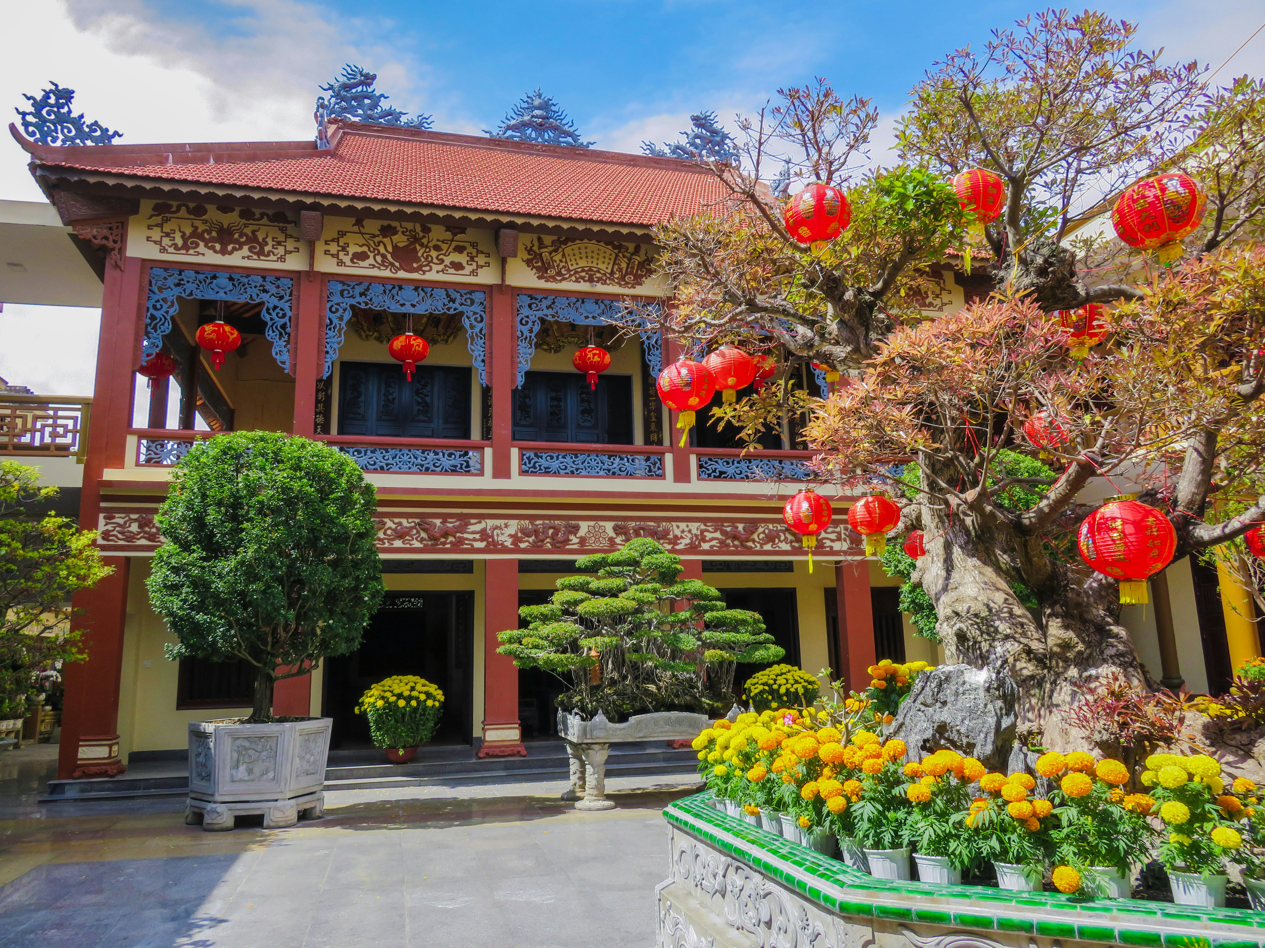 Traditional Vietnamese building adorned with red lanterns and vibrant flowers under a sunny sky.