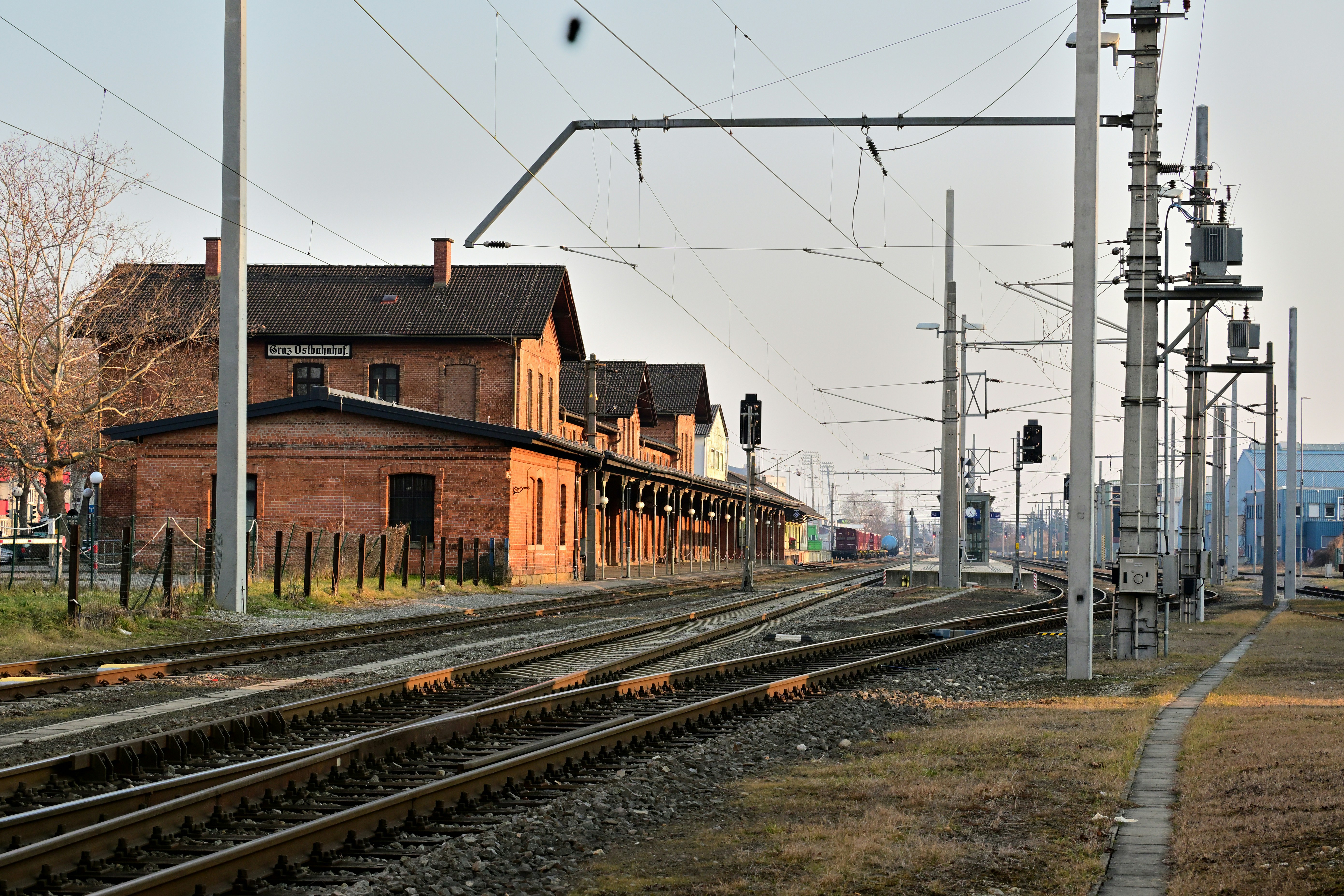 Railway tracks leading to a brick industrial building under a clear sky.