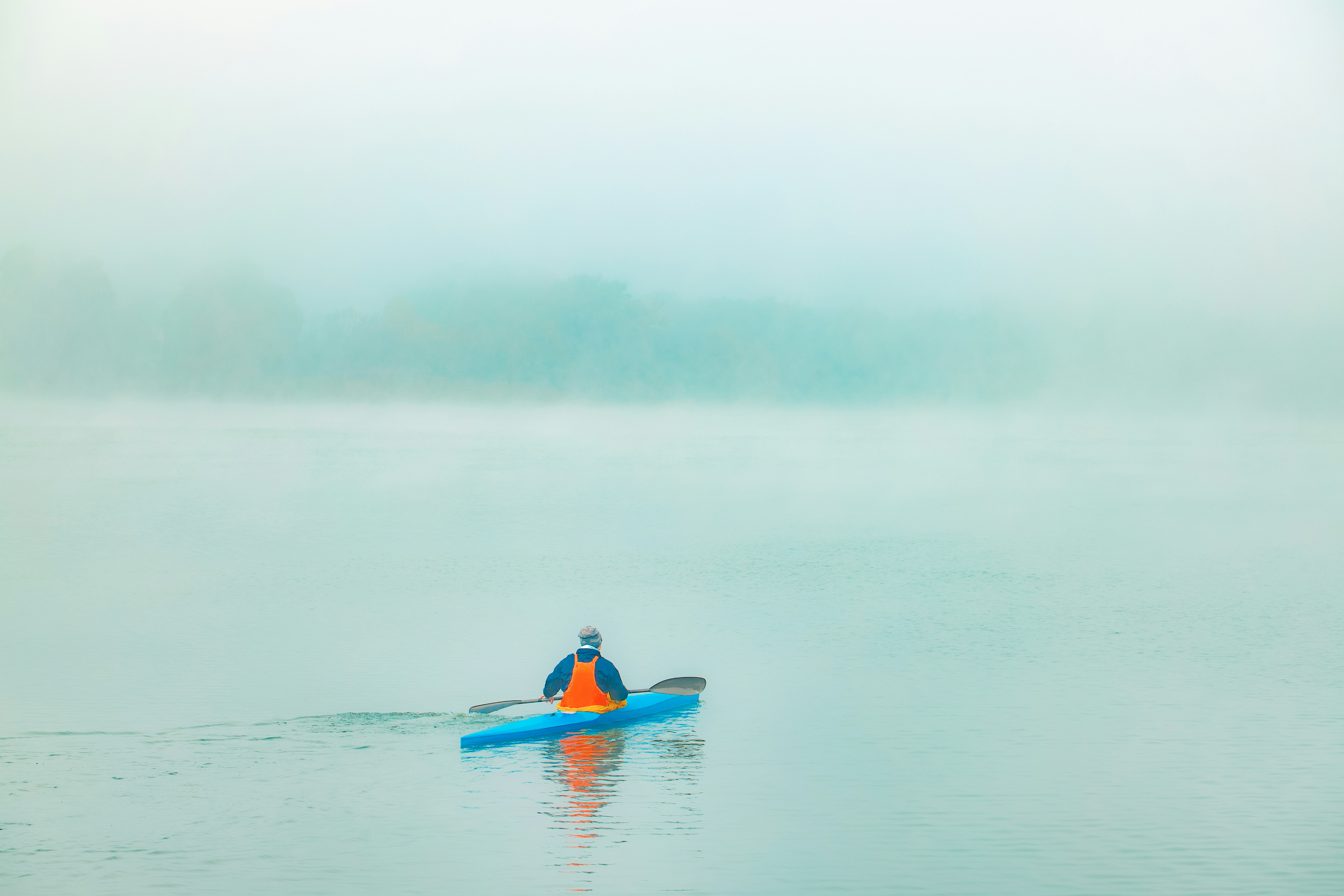 Kayaker glides through foggy waters on a frosty morning, surrounded by a serene, mist-covered landscape.