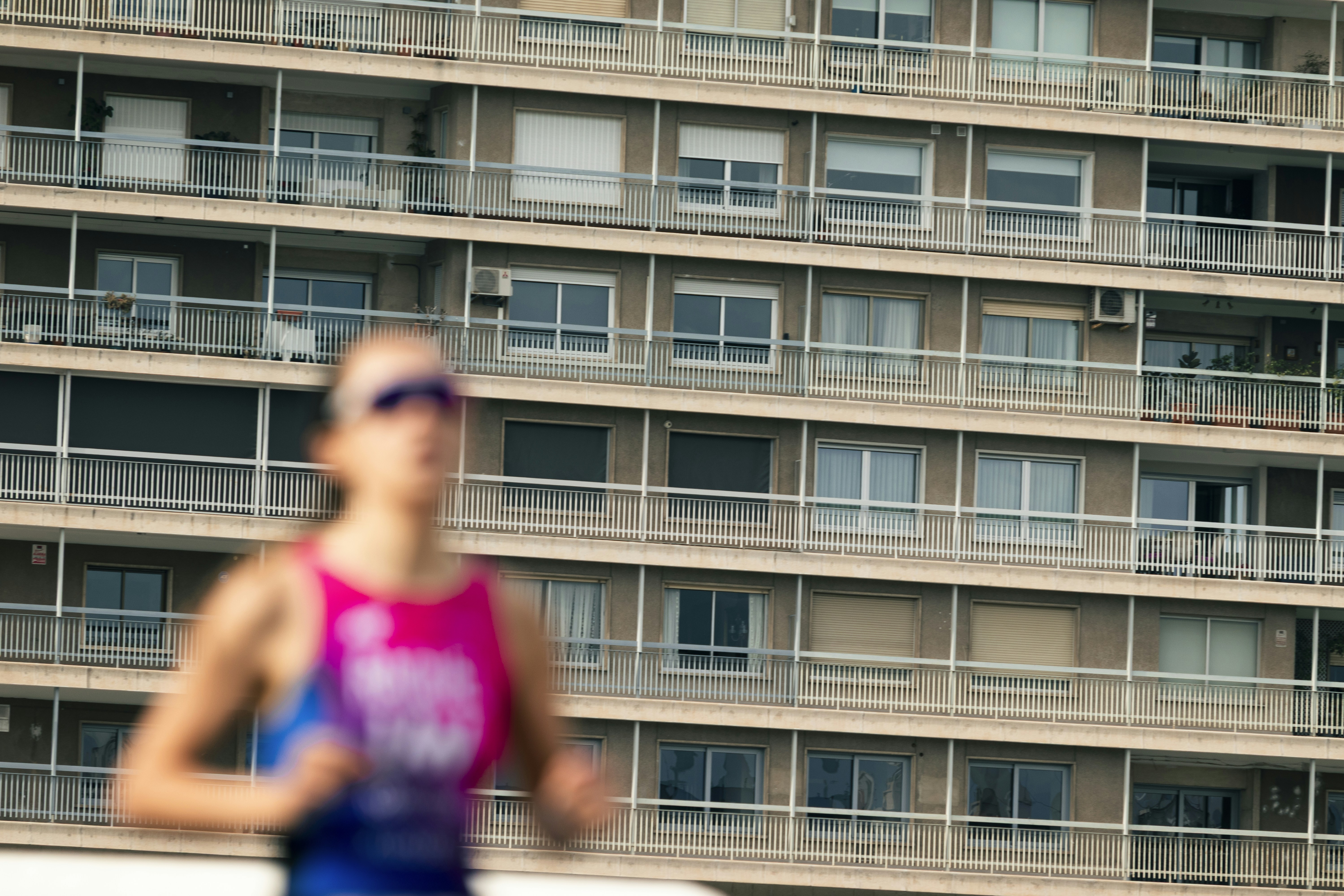 Blurred runner in a vibrant outfit against a backdrop of uniform apartment balconies.