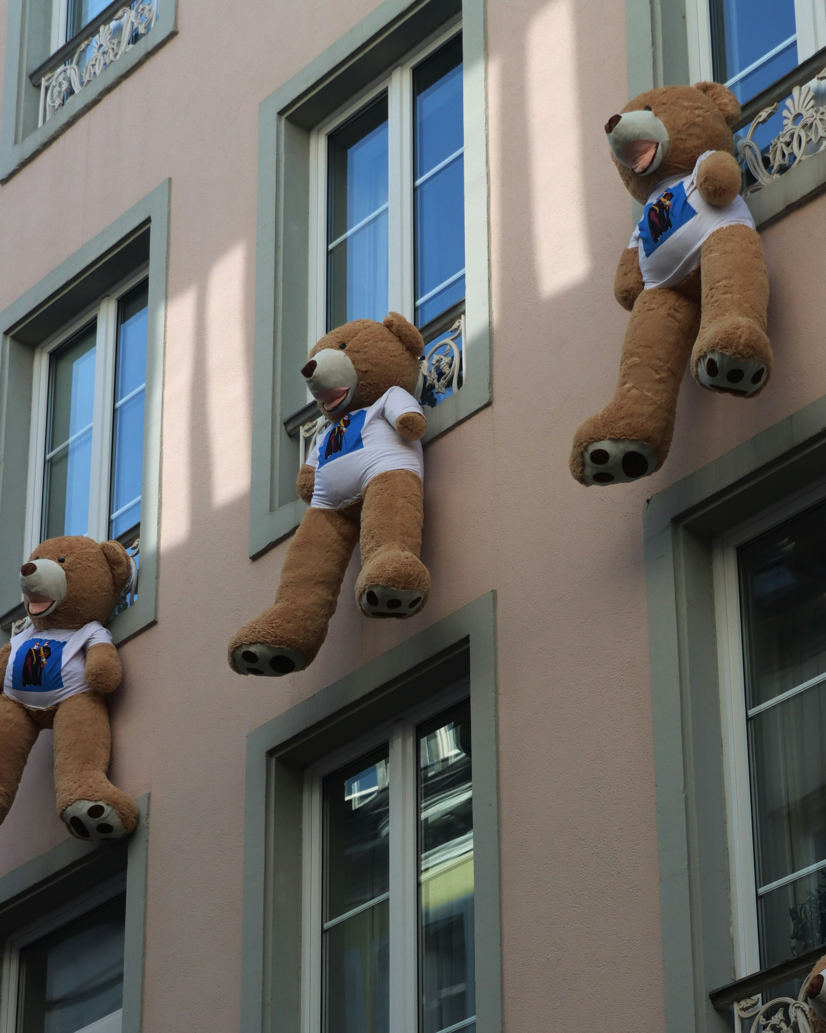 Three Giant Teddy Bears Cling to a Pink City Facade