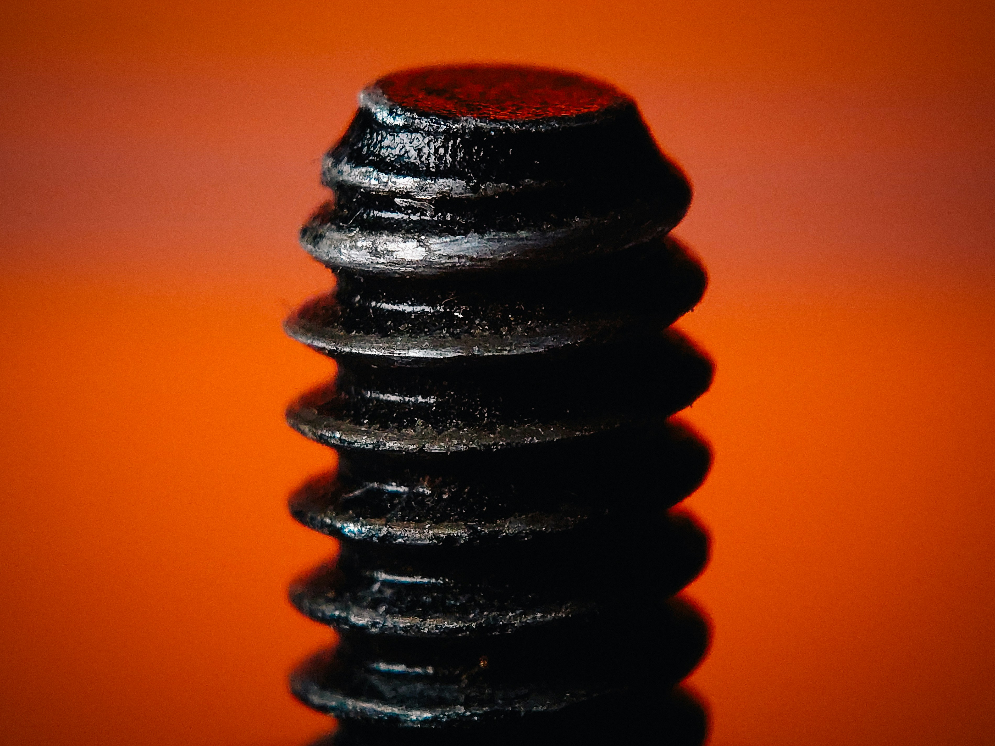 Close-up of a black bolt thread against a warm, orange background.
