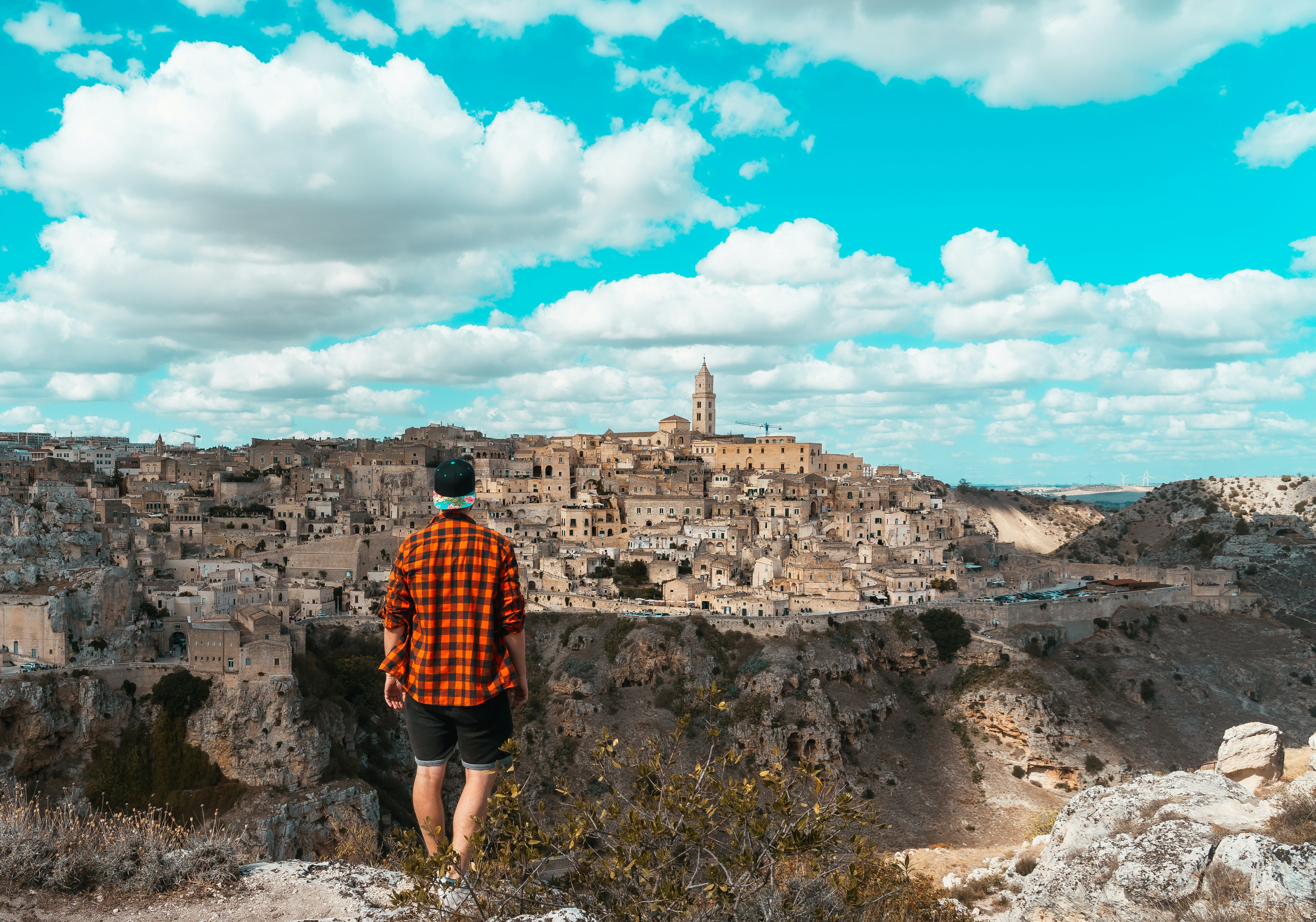 Person overlooking the ancient cityscape of Matera under a vibrant sky.