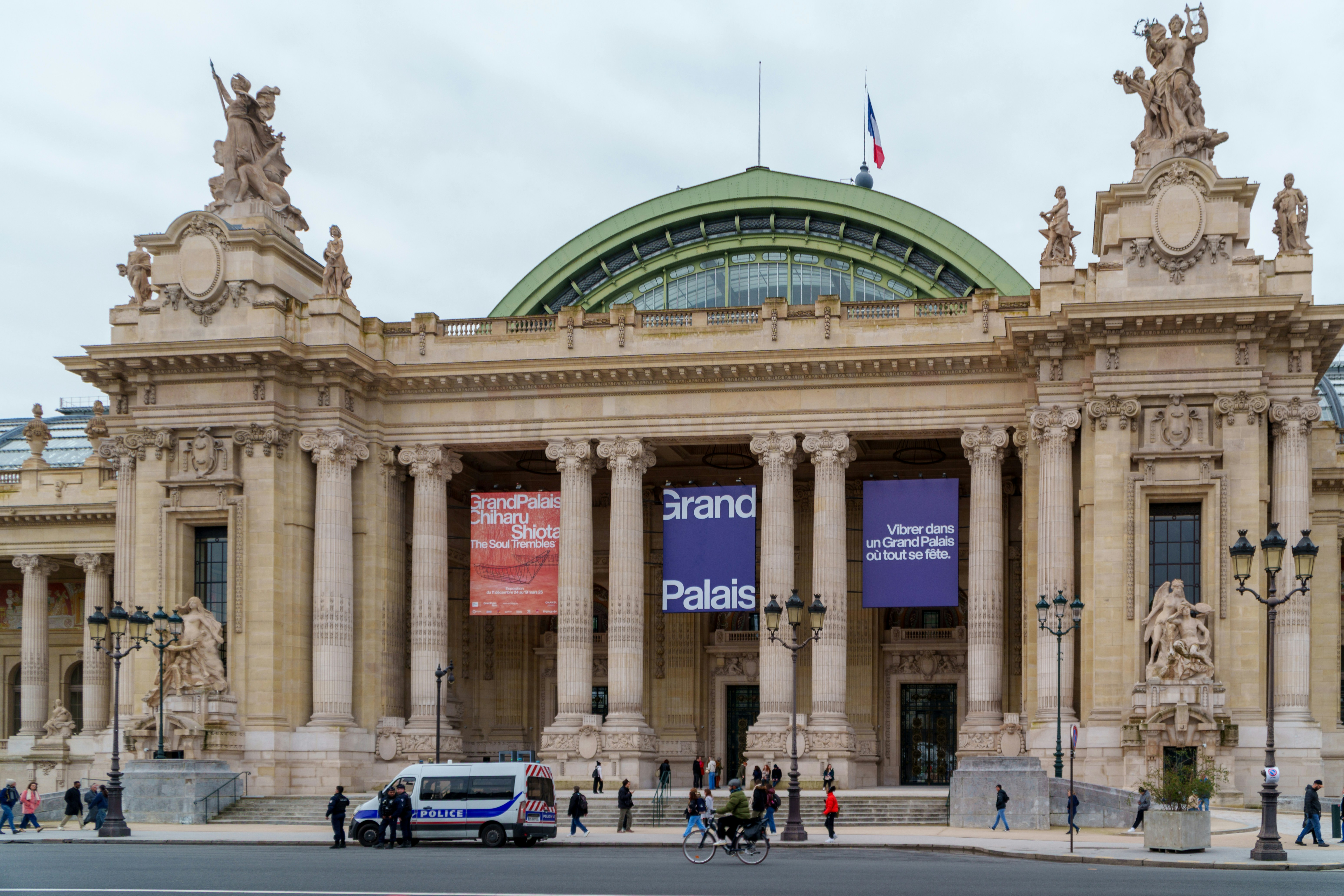 Historic stone facade of the Grand Palais adorned with colorful banners and intricate sculptures.