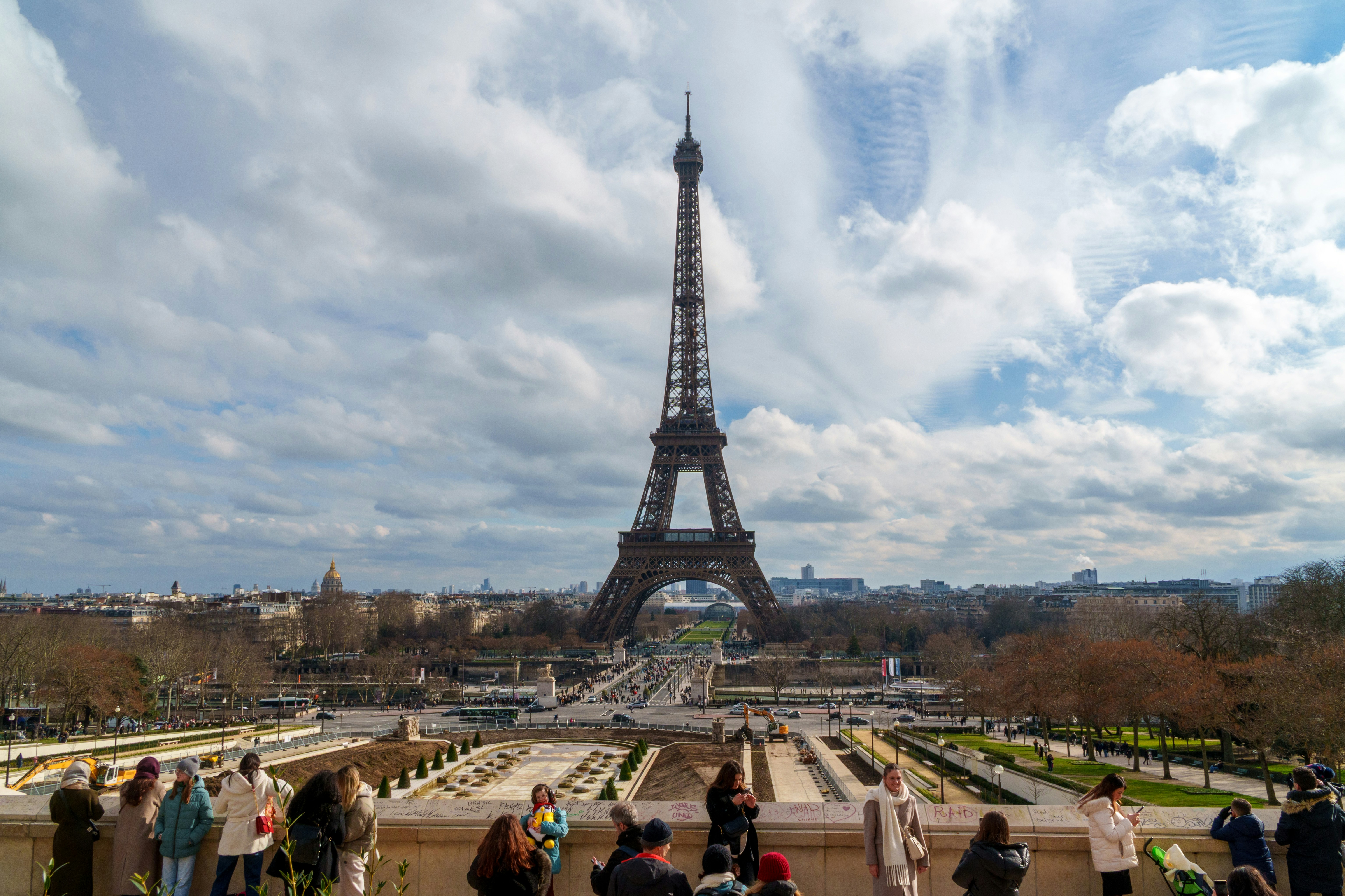 Eiffel Tower framed by lush parks and a dramatic cloudy sky, viewed from across the Seine.