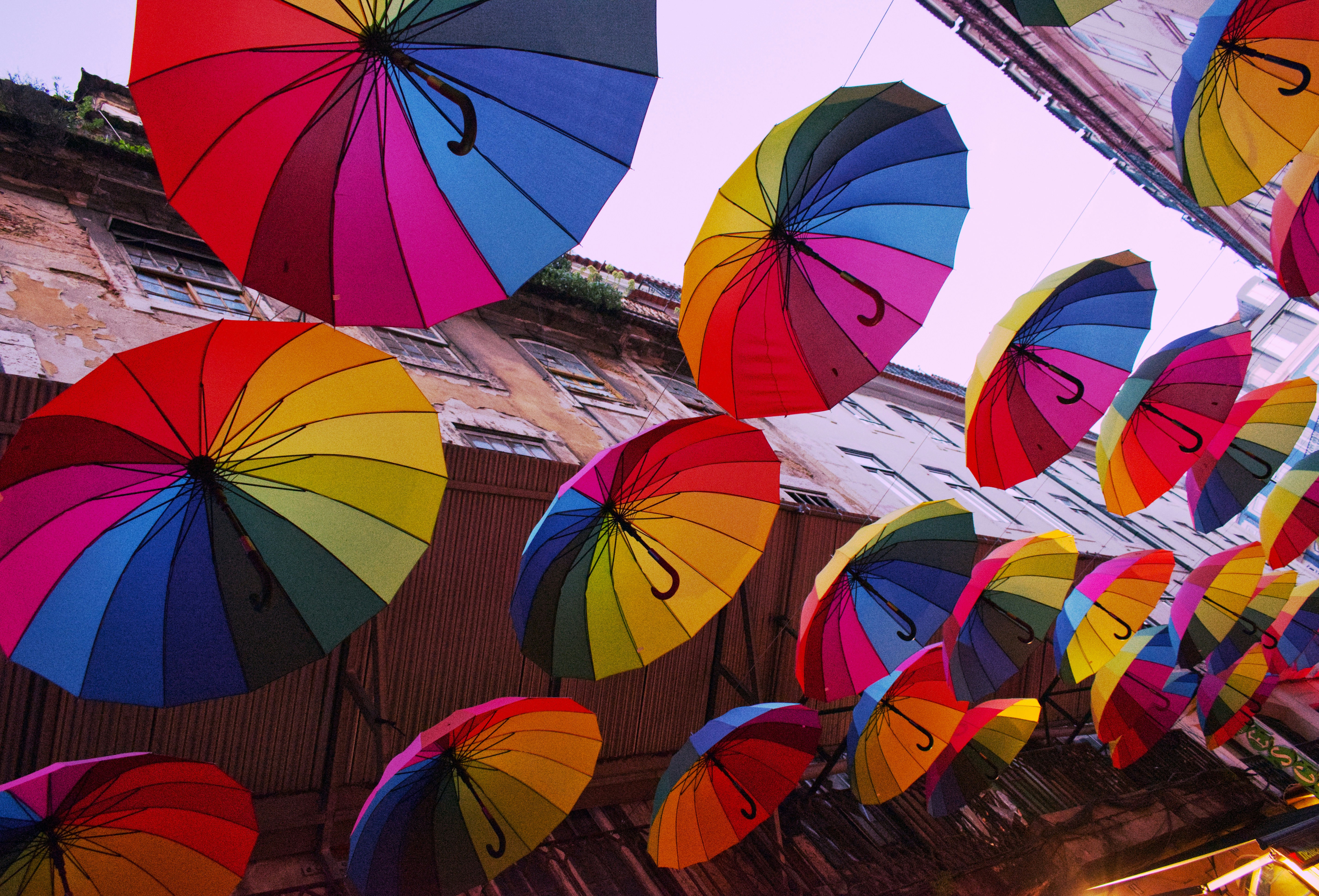 Vibrant umbrellas suspended between buildings create a colorful canopy against the sky.