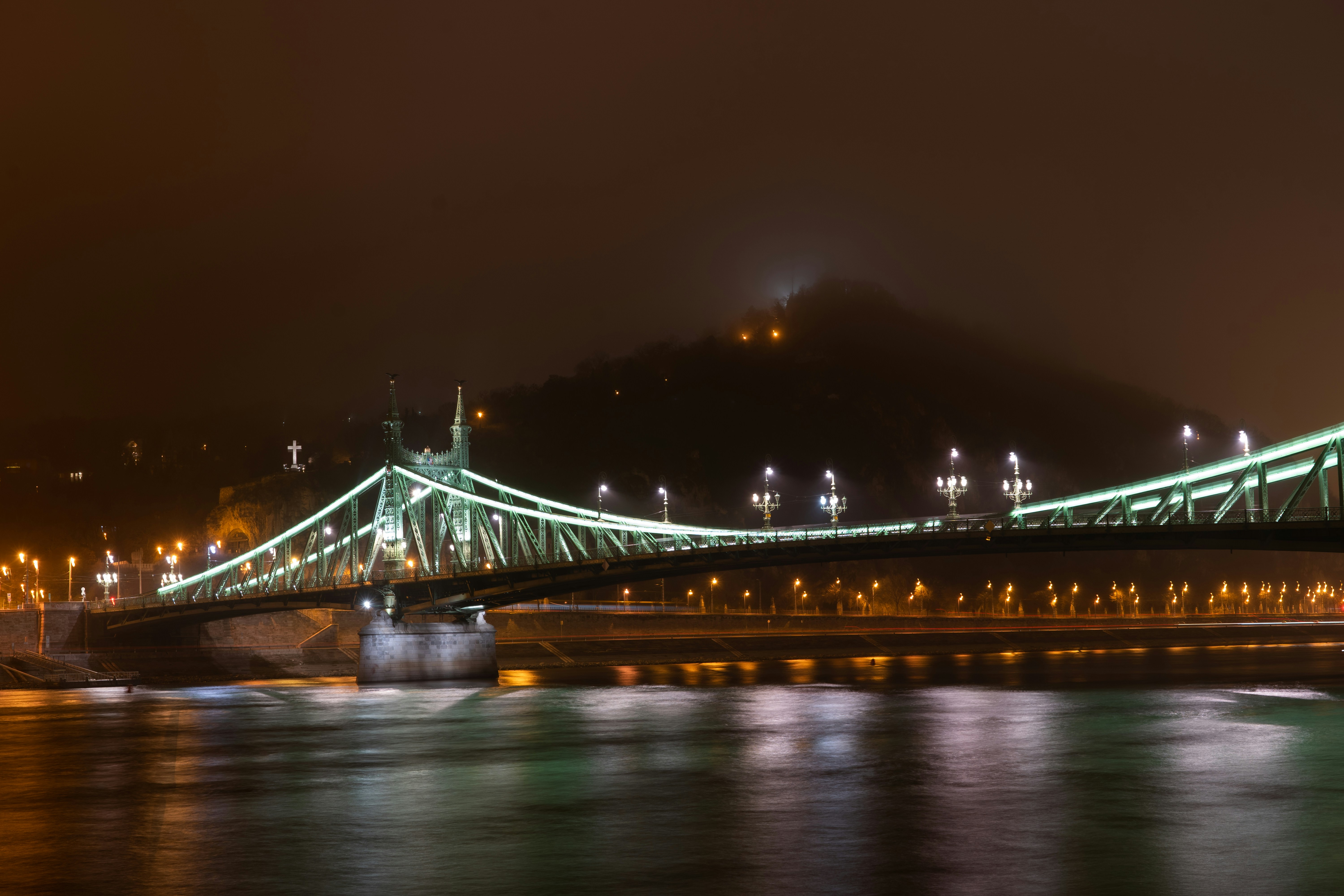 Illuminated Suspension: Night River Crossing Beneath a Misty Hill