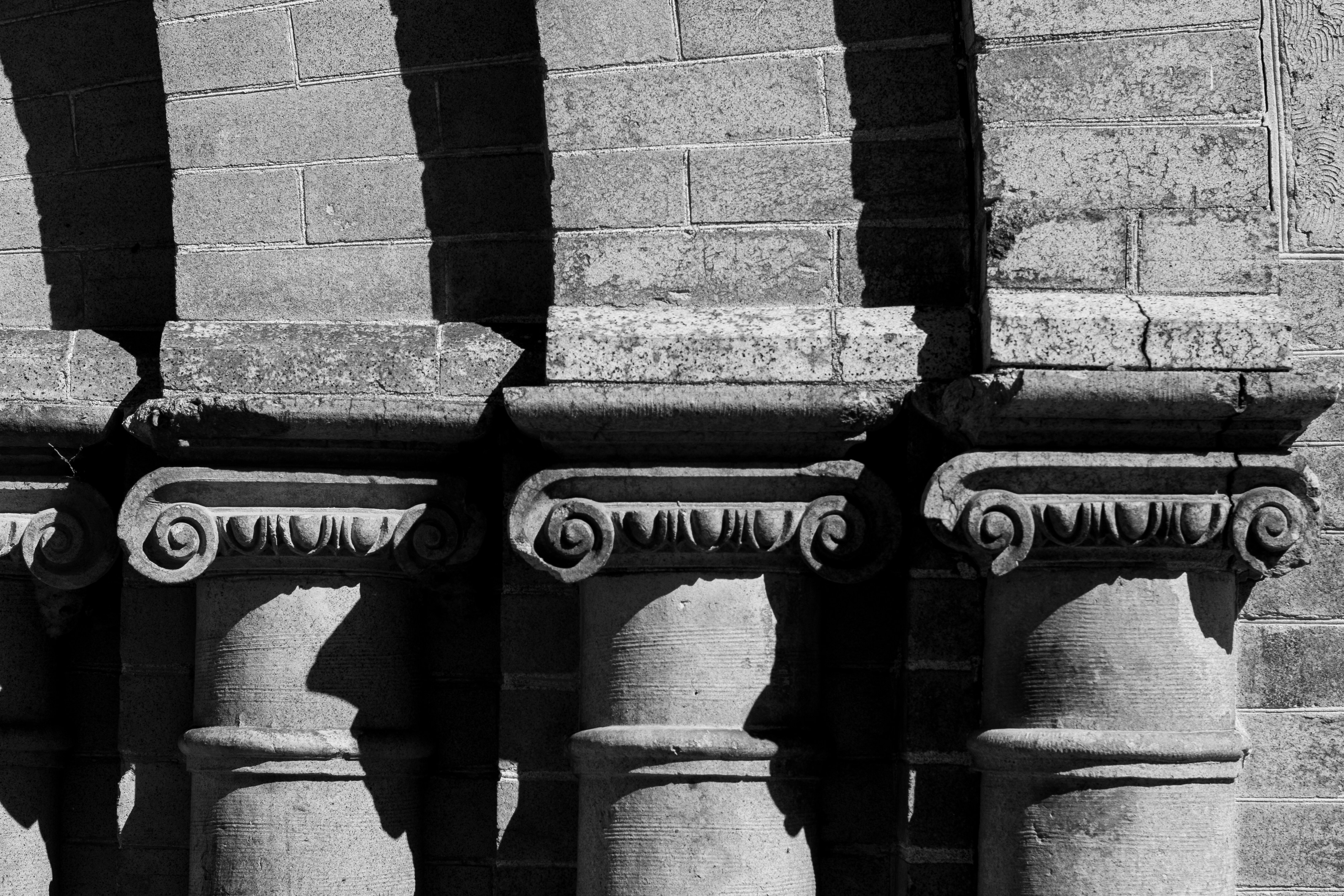 Ornate stone columns with intricate capitals cast dramatic shadows against a brick wall.