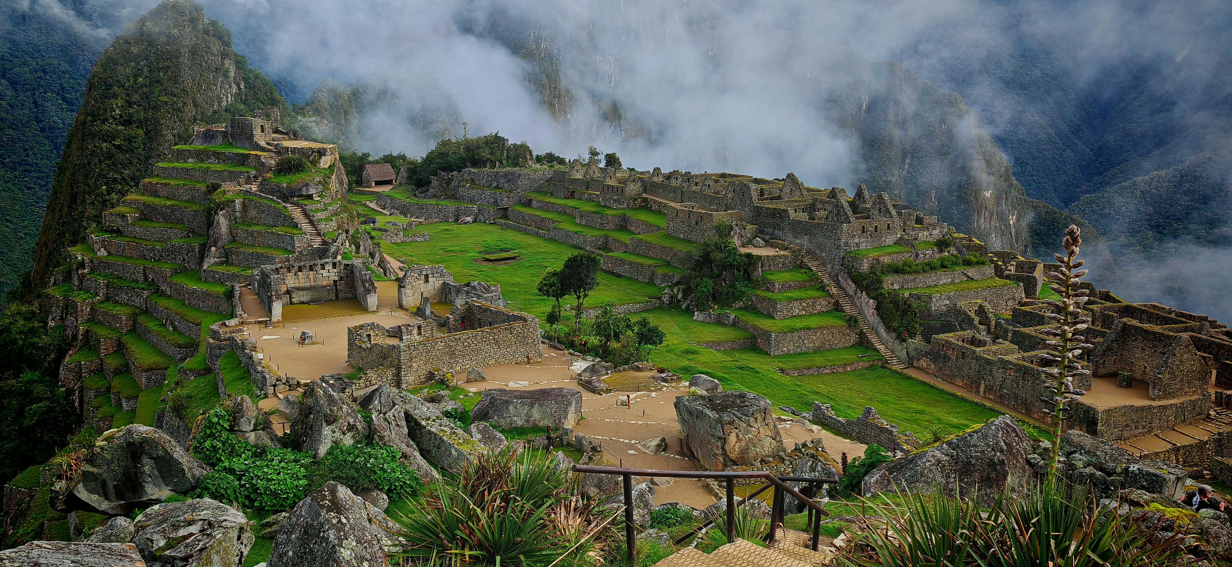 Machu Picchu's terraced ruins rise amidst the clouds, showcasing the intricate architecture and lush greenery of the Andes. The scene evokes a sense of mystery and history.