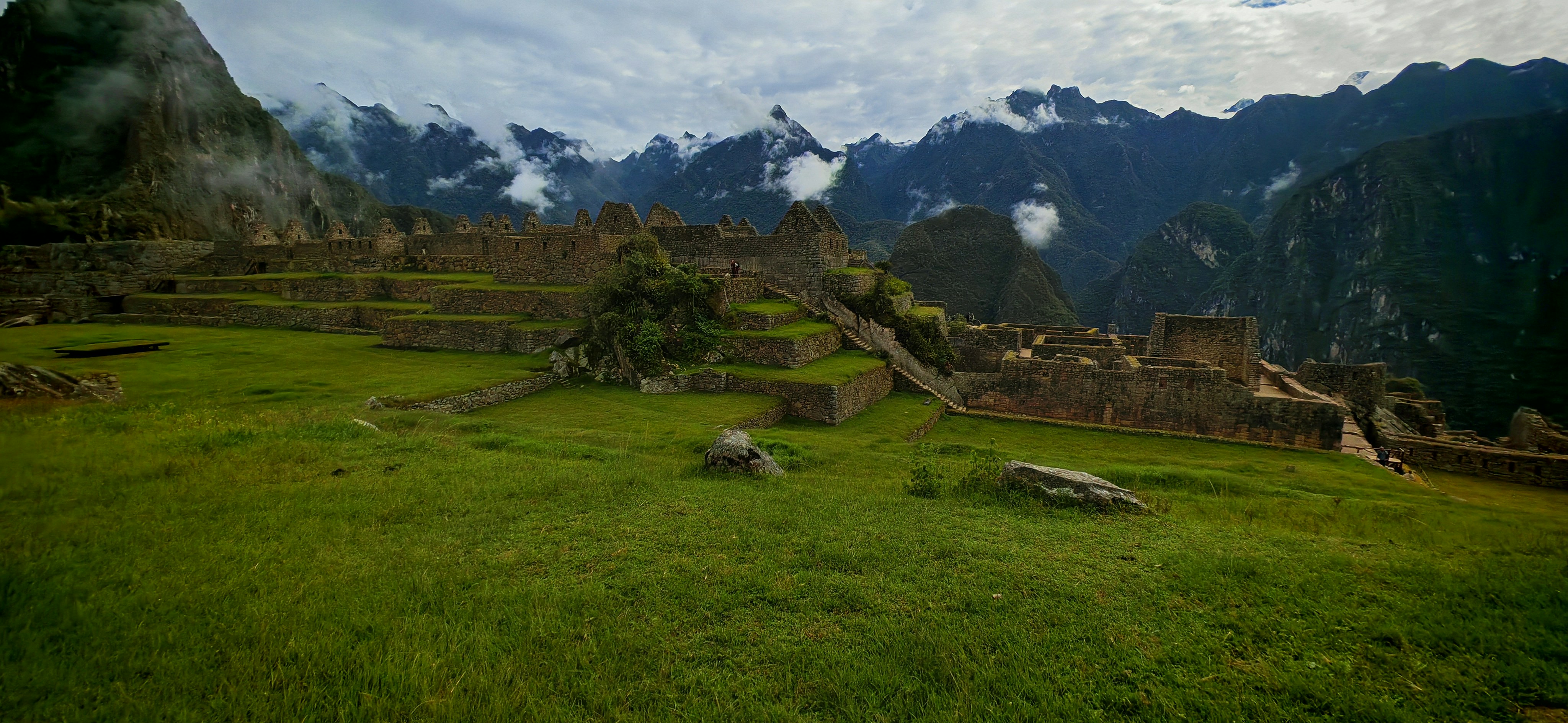 Terraced Inca ruins on a grassy plateau with misty Andean peaks in the background.