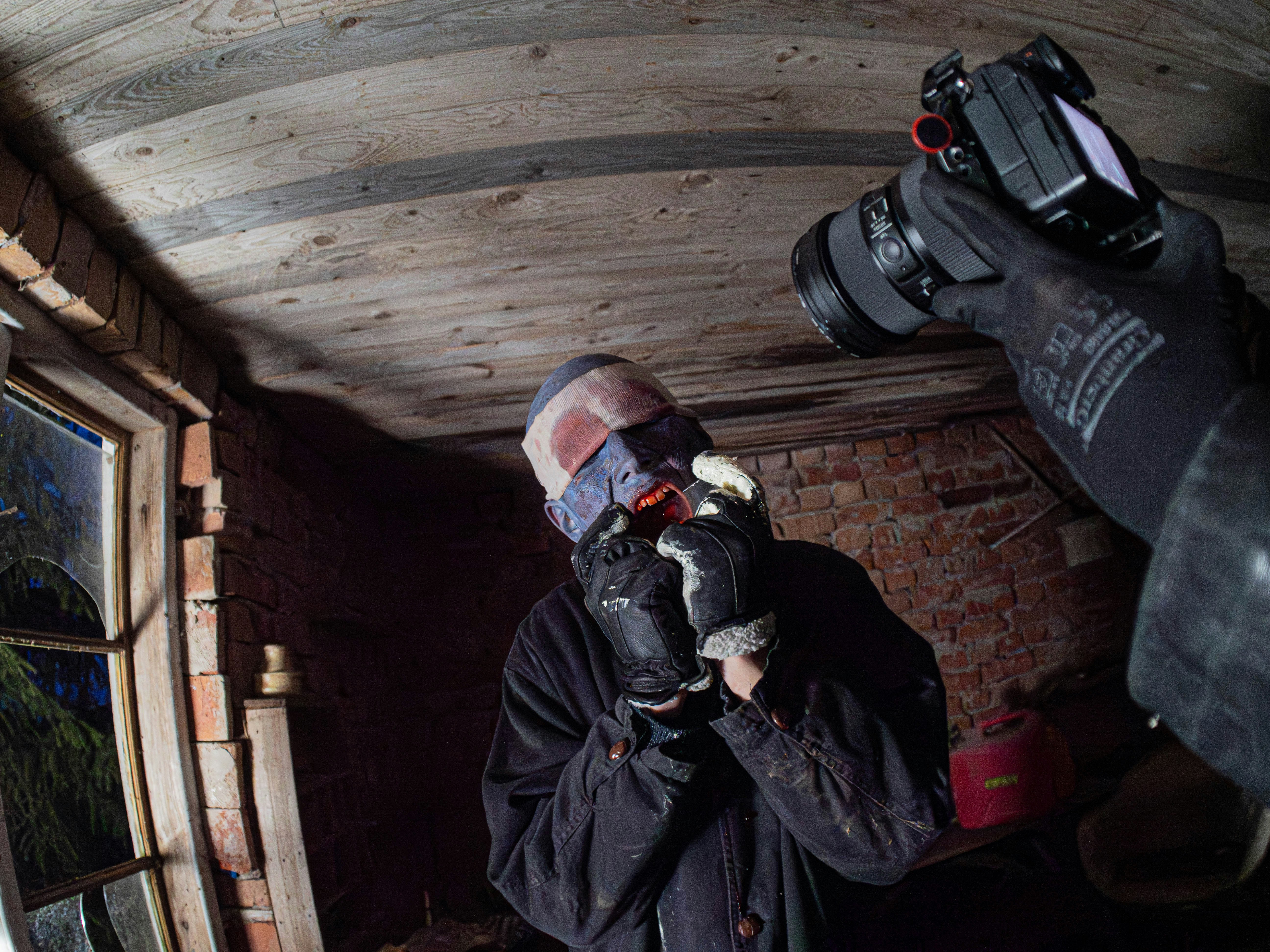 Masked figure in a dimly lit rustic room capturing a self-portrait.