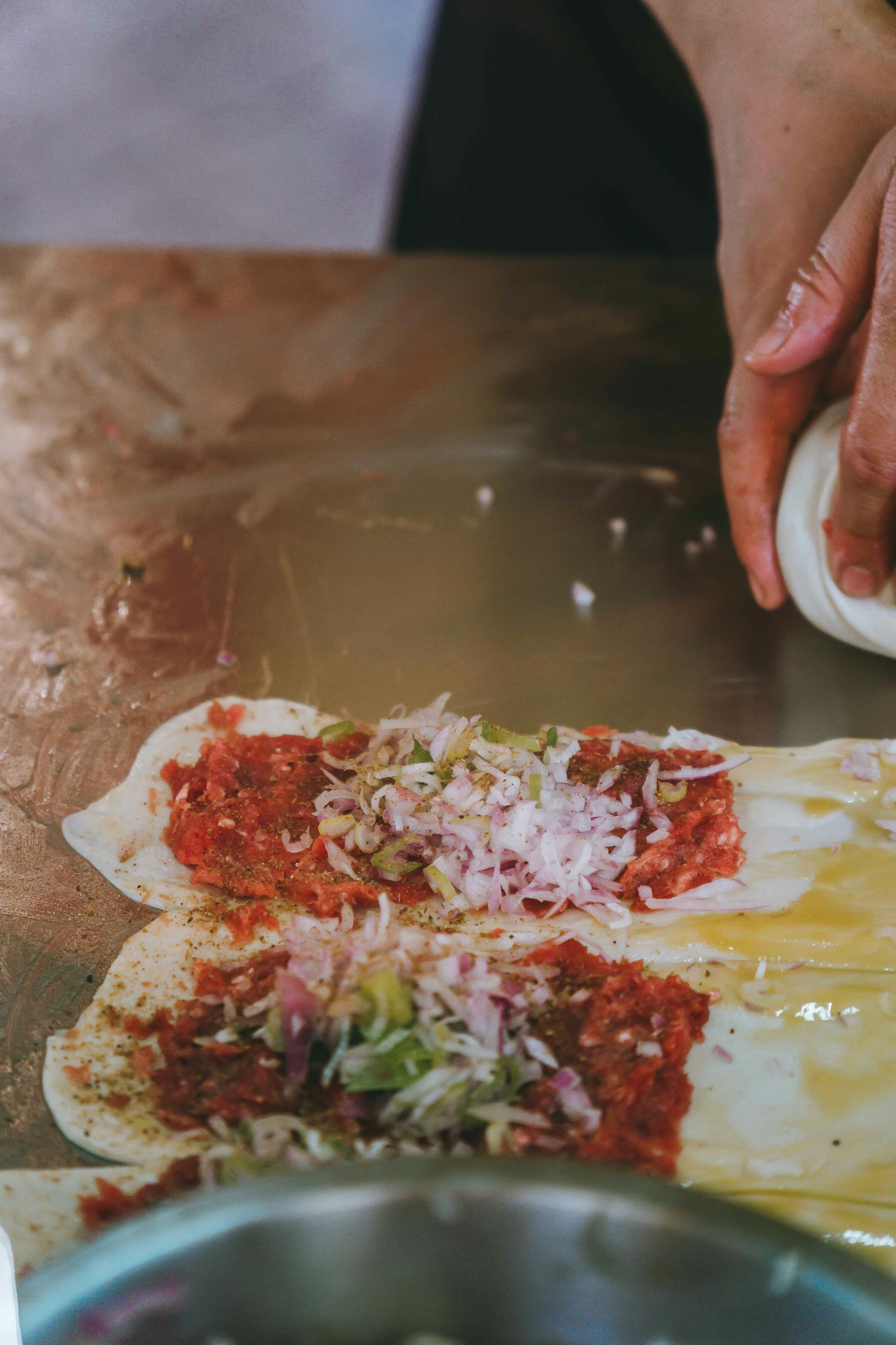 Copper-Plate Taco Assembly: Red Salsa, Diced Onions, and Melted Cheese on a Shiny Prep Table