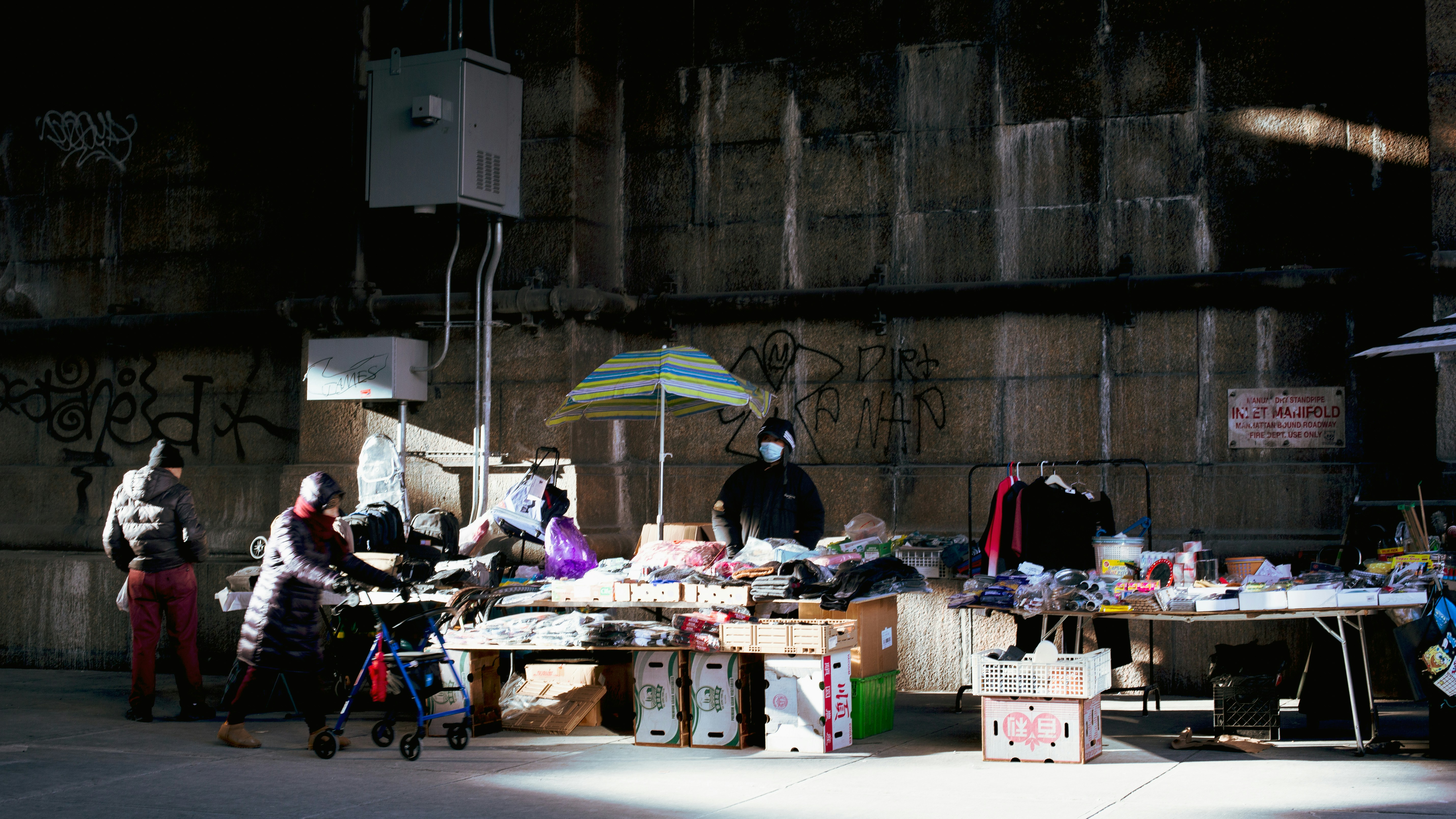 Street vendors under a bridge with vibrant goods and contrasting light.