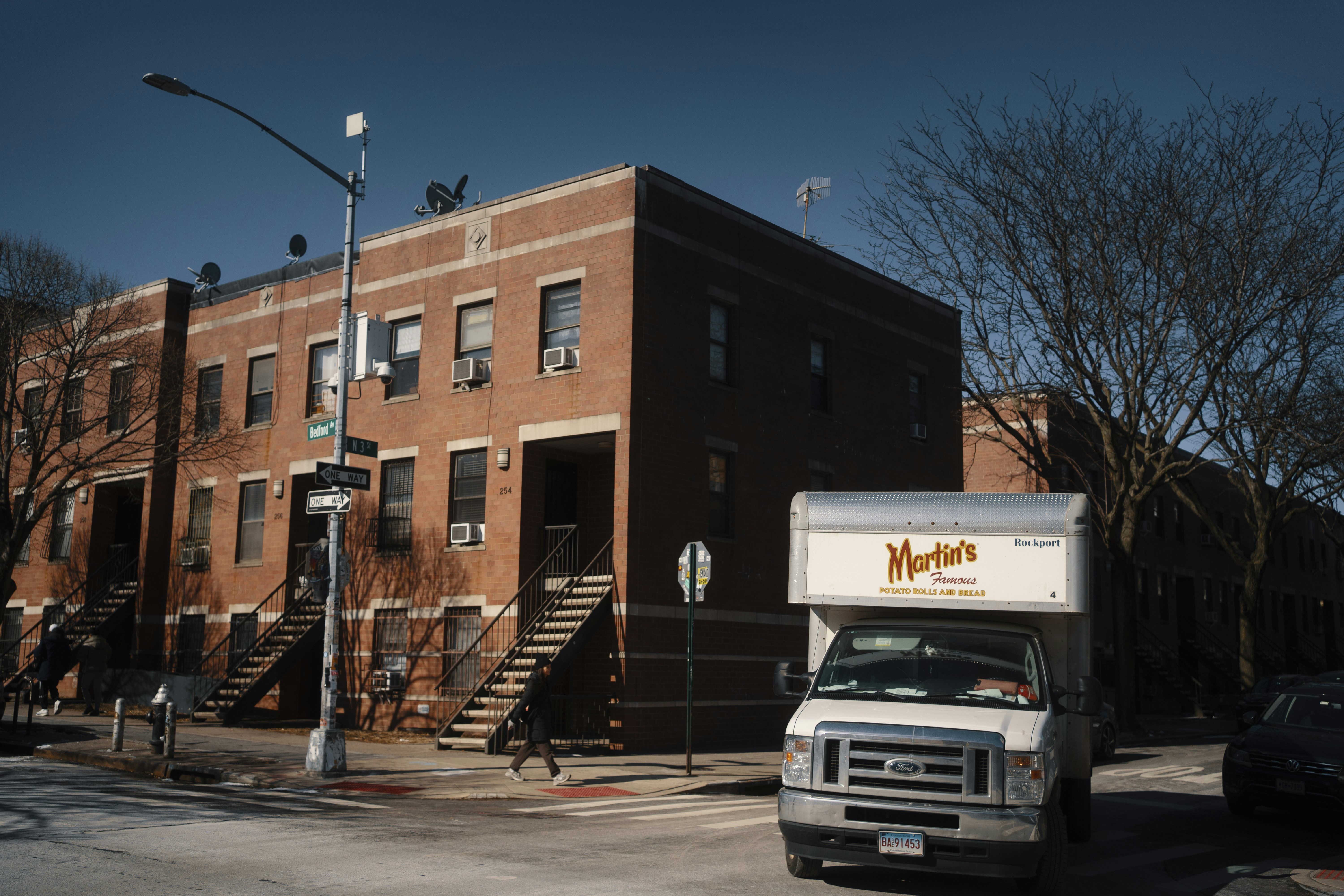 Corner of a city street featuring a brick building and parked moving truck under a clear blue sky.