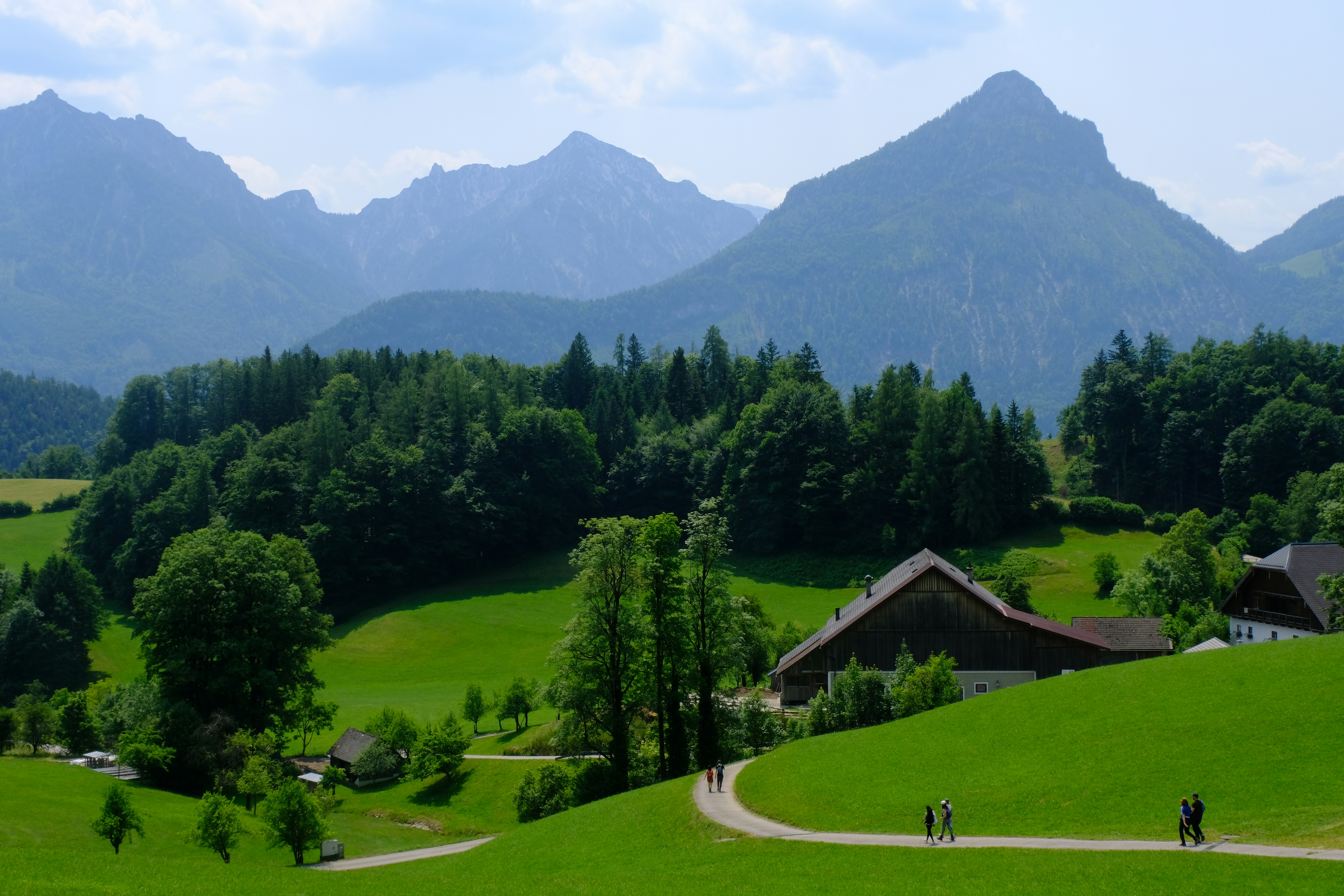 Verdant hills and rustic buildings set against rugged mountains under a bright sky.