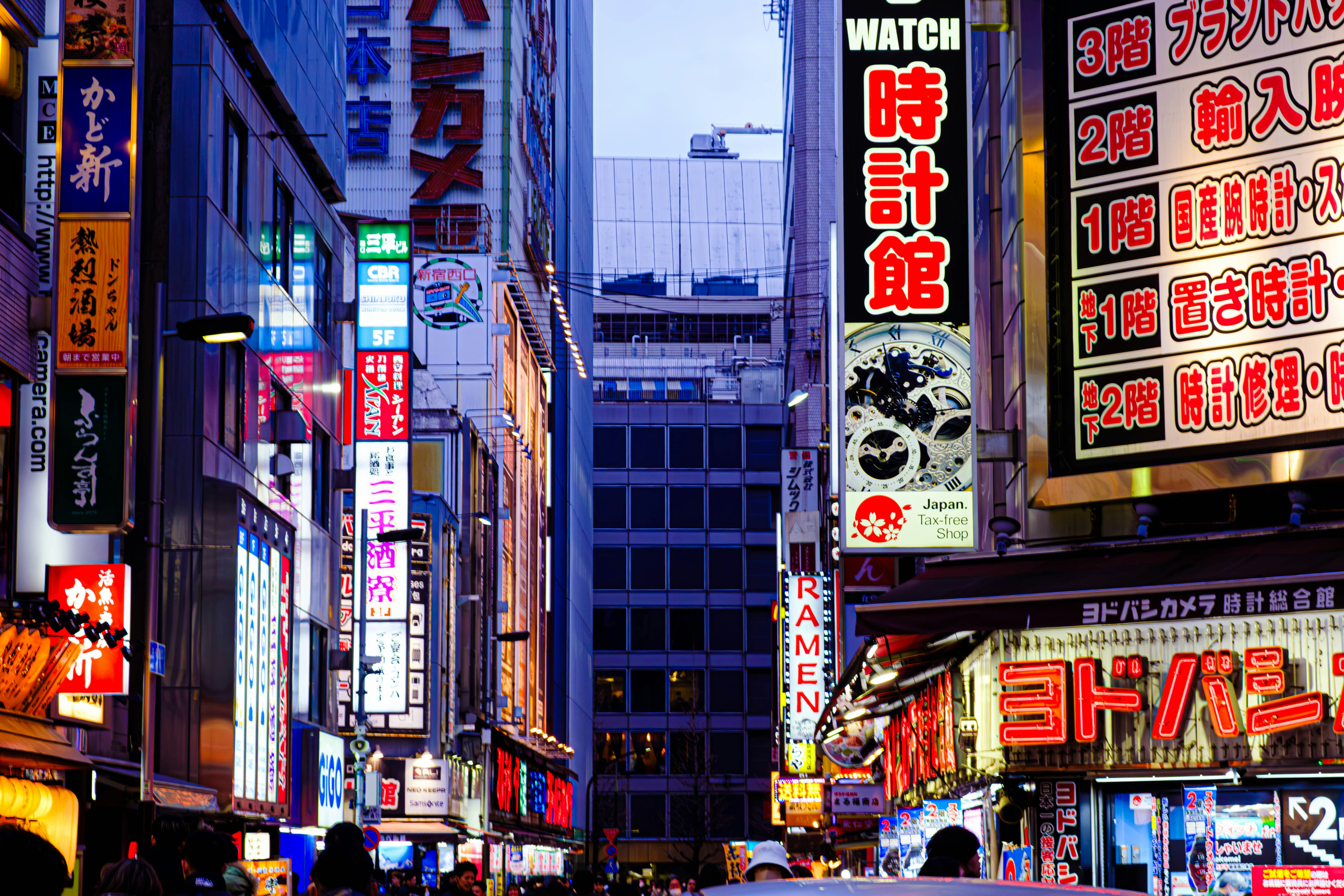 Colorful neon signs illuminate a bustling urban street in Shinjuku at twilight.