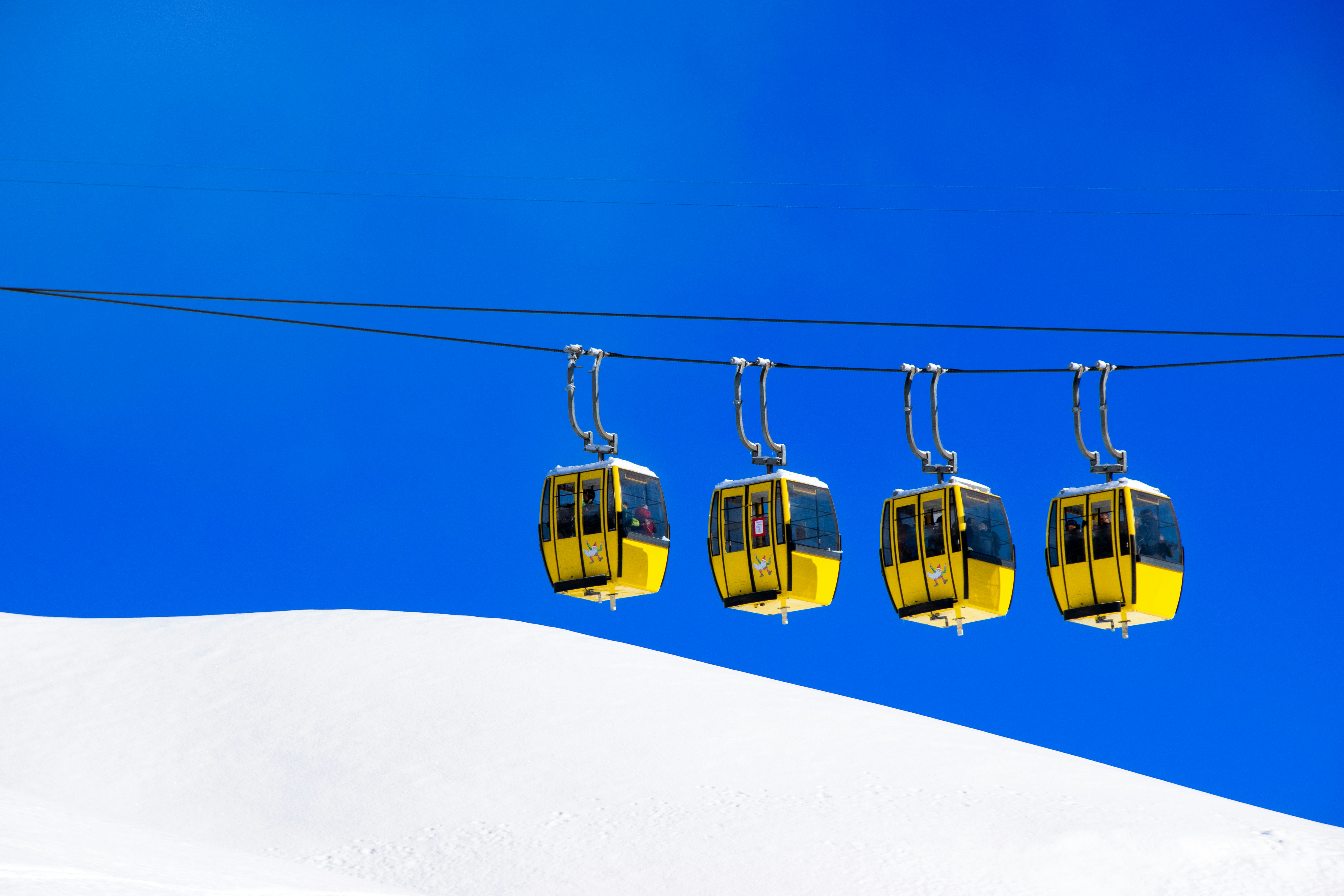 Yellow cable cars glide over snowy hills under a vibrant blue sky.