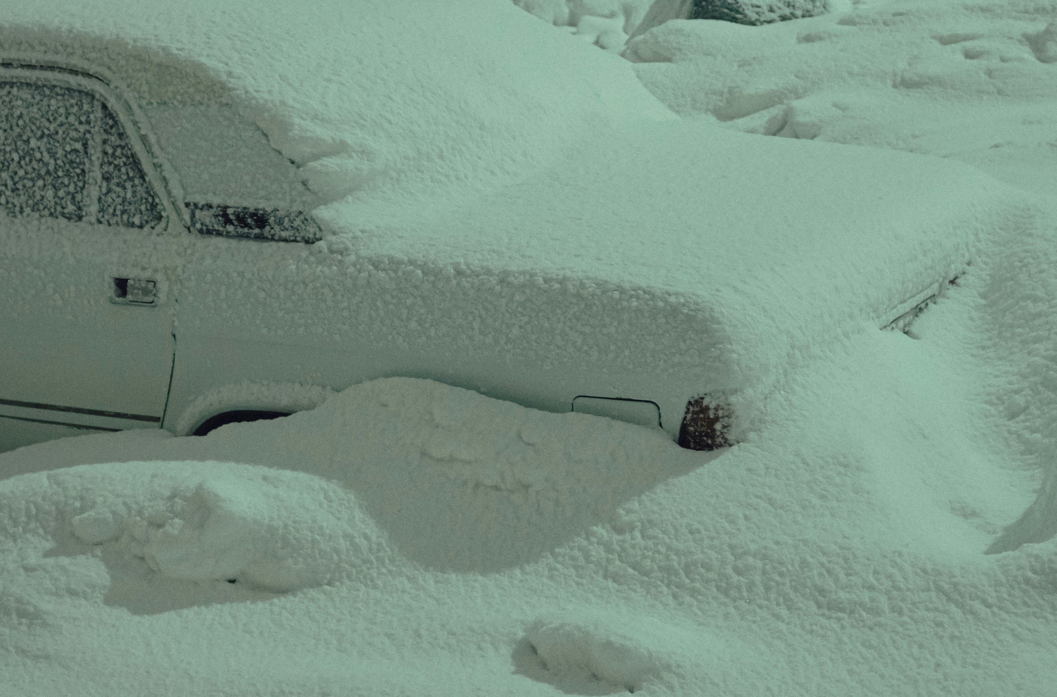 Car buried under a thick layer of snow, with only the outline visible.