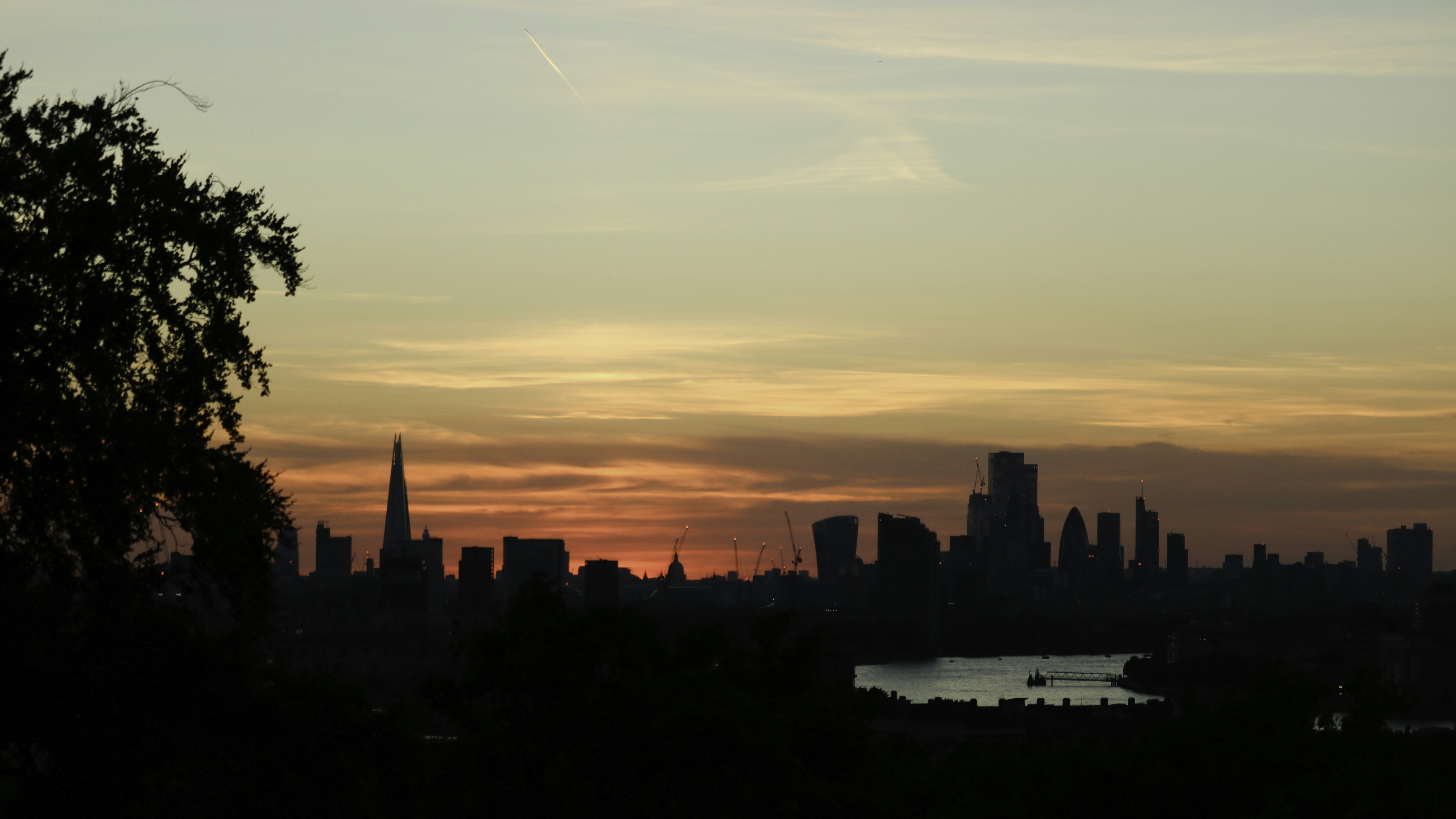 London skyline silhouetted against a vibrant orange and pink sunset sky.