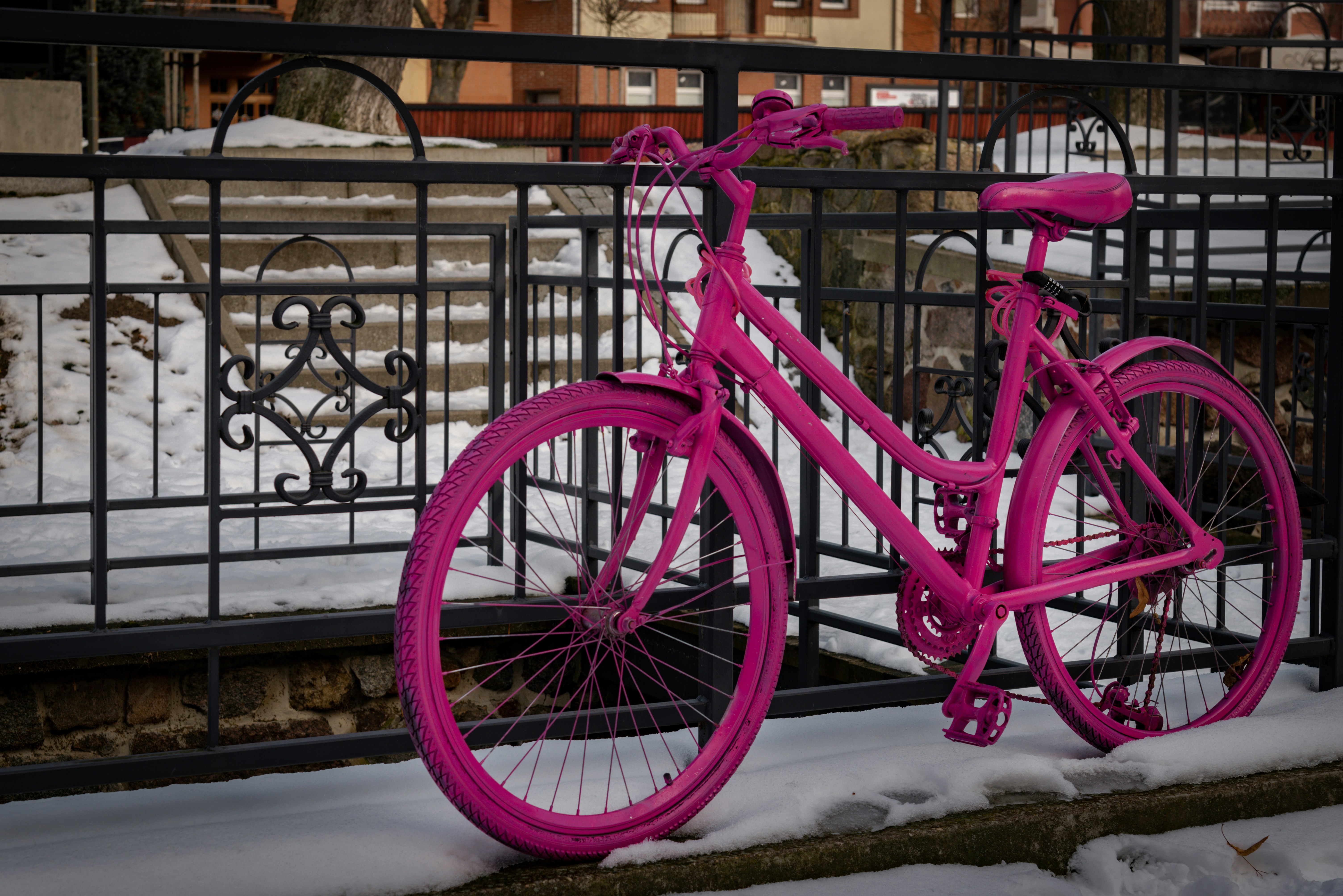 Neon Pink Bicycle Leaning Against a Snow-Swept Iron Rail