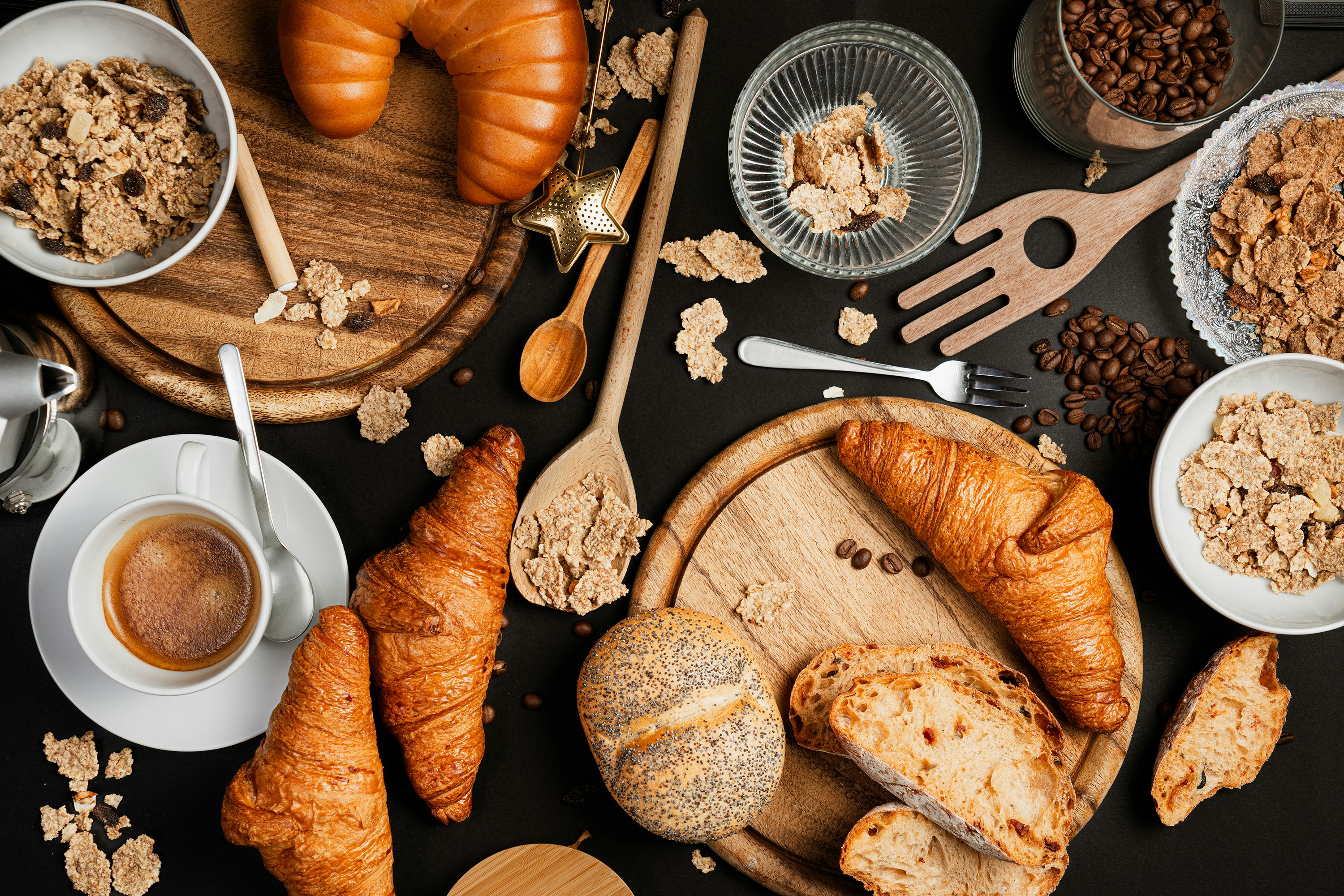 Assortment of croissants, bread, and cereal with coffee on a dark background.