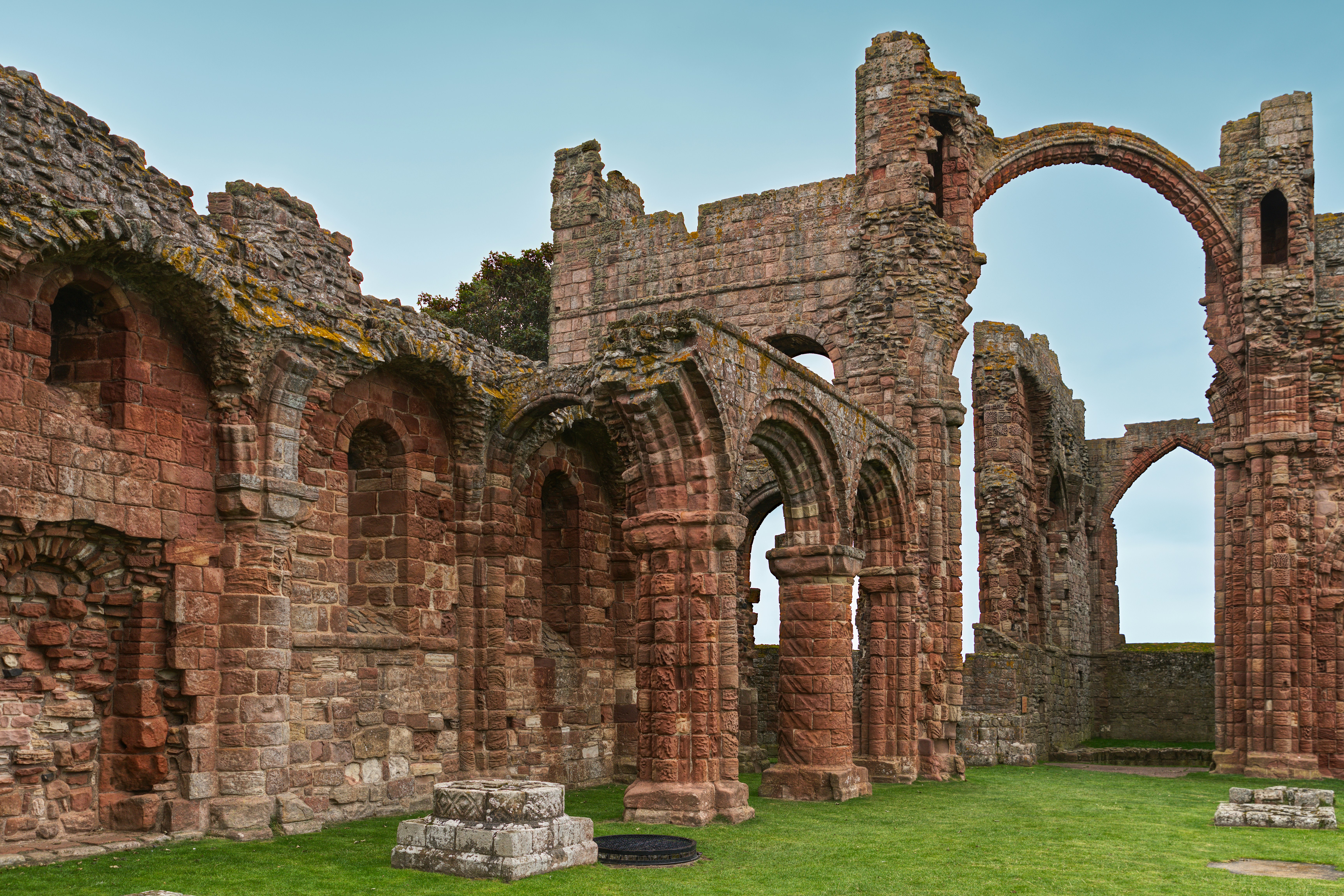 Ruins of a medieval stone structure with arches and columns against a clear sky.