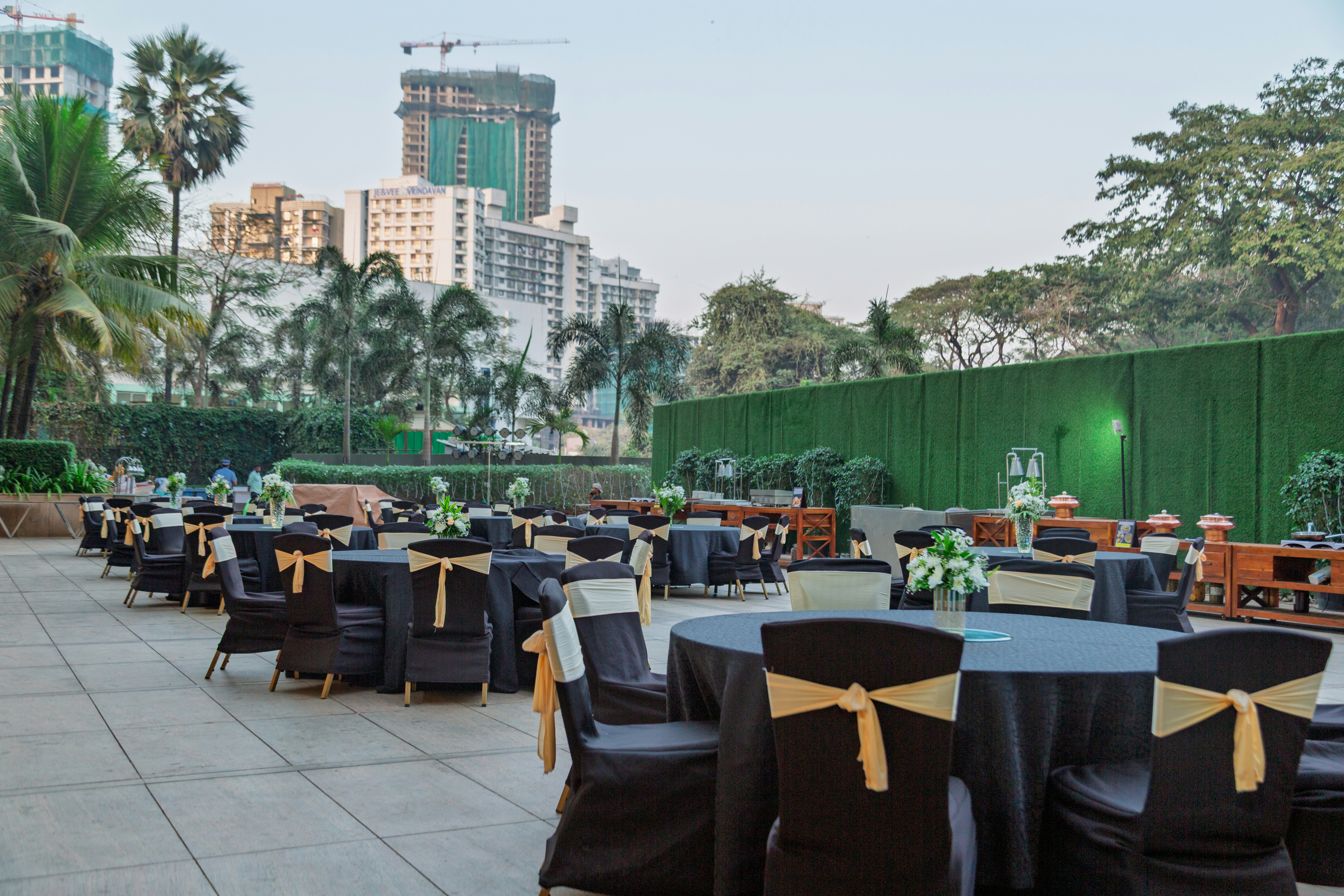 Chic outdoor dining area with black chairs adorned with gold bows amidst urban skyscrapers.
