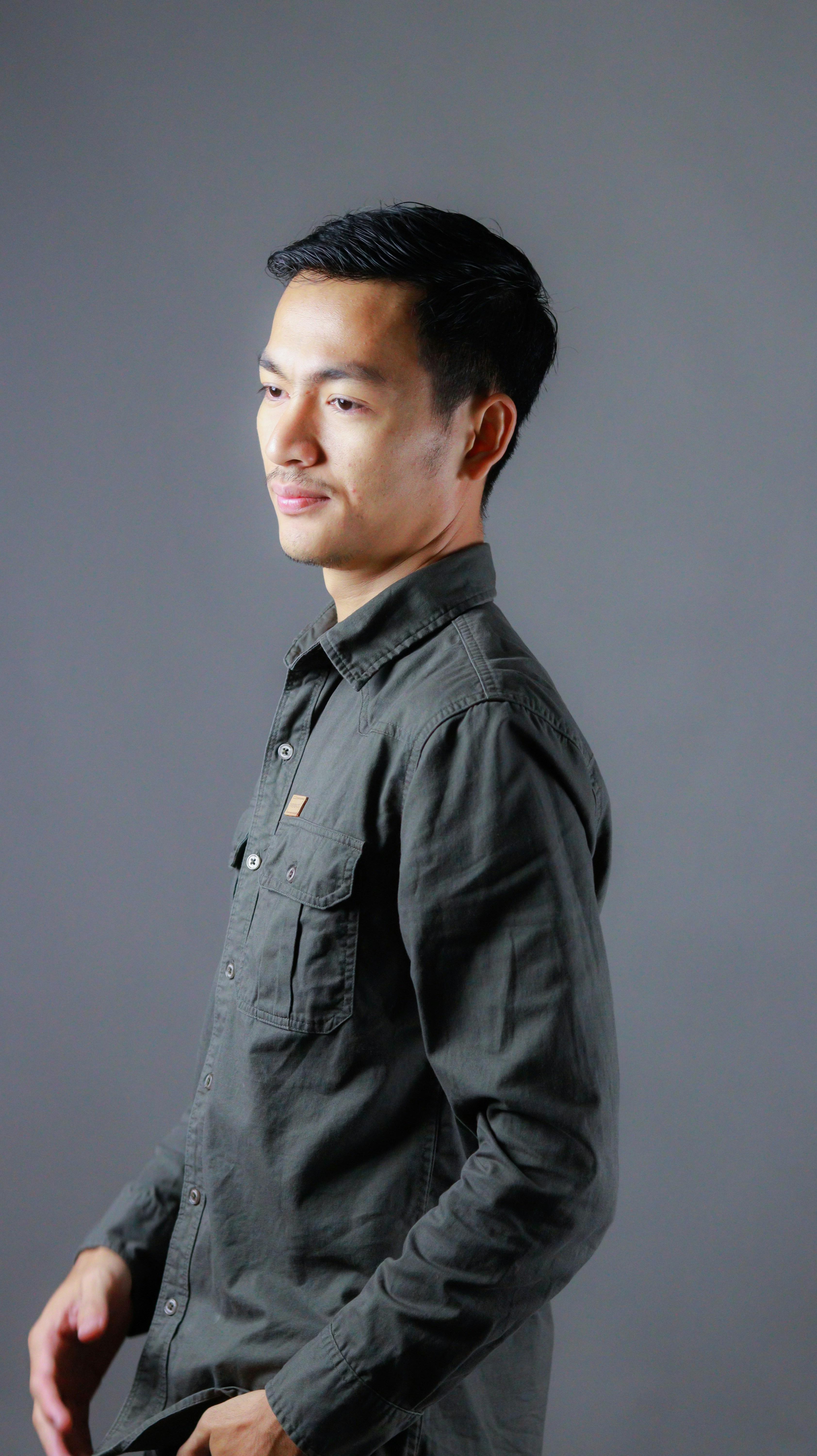 A young man in a dark shirt poses thoughtfully against a muted gray backdrop.